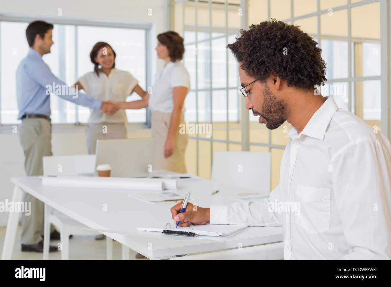 Businessman writing notes with colleagues shaking hands in office Stock ...