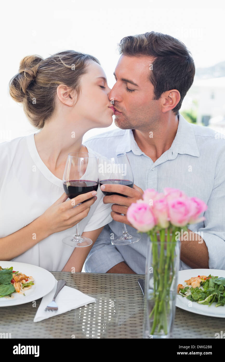 Couple kissing as they hold wine glasses at food table Stock Photo - Alamy