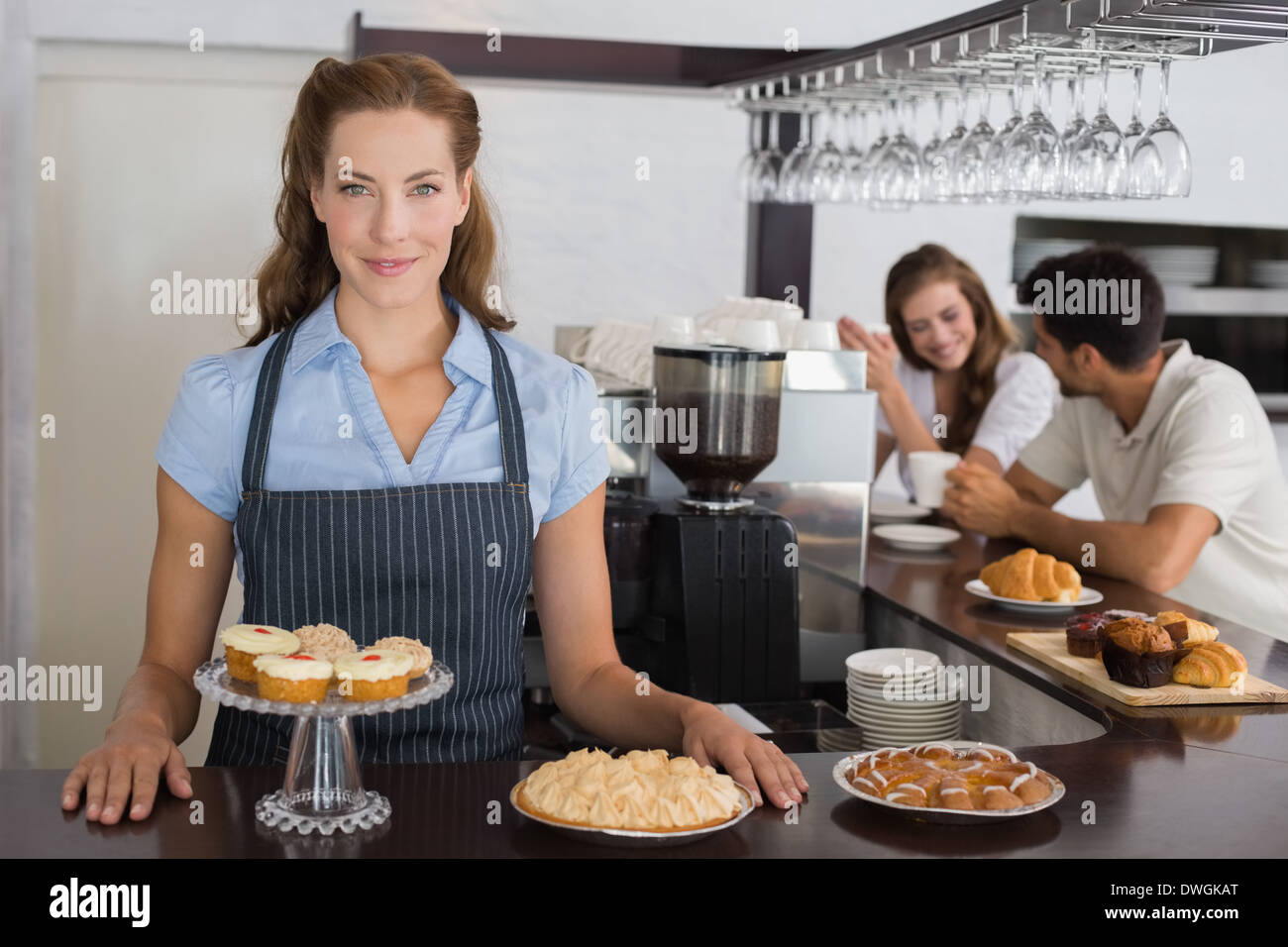 Smiling cafe owner with sweet snacks and couple at counter in coffee ...