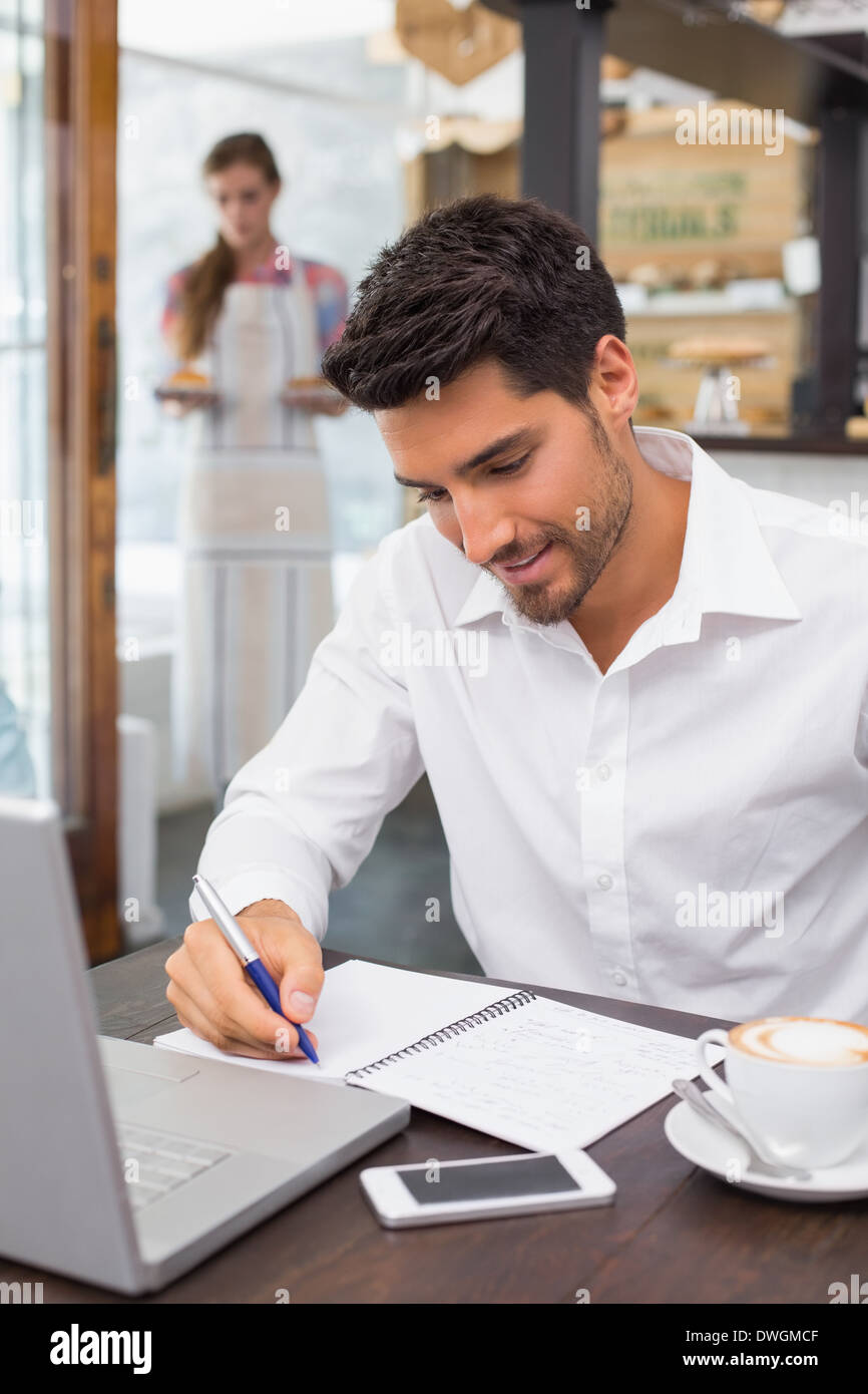 Man writing notes with laptop in coffee shop Stock Photo - Alamy