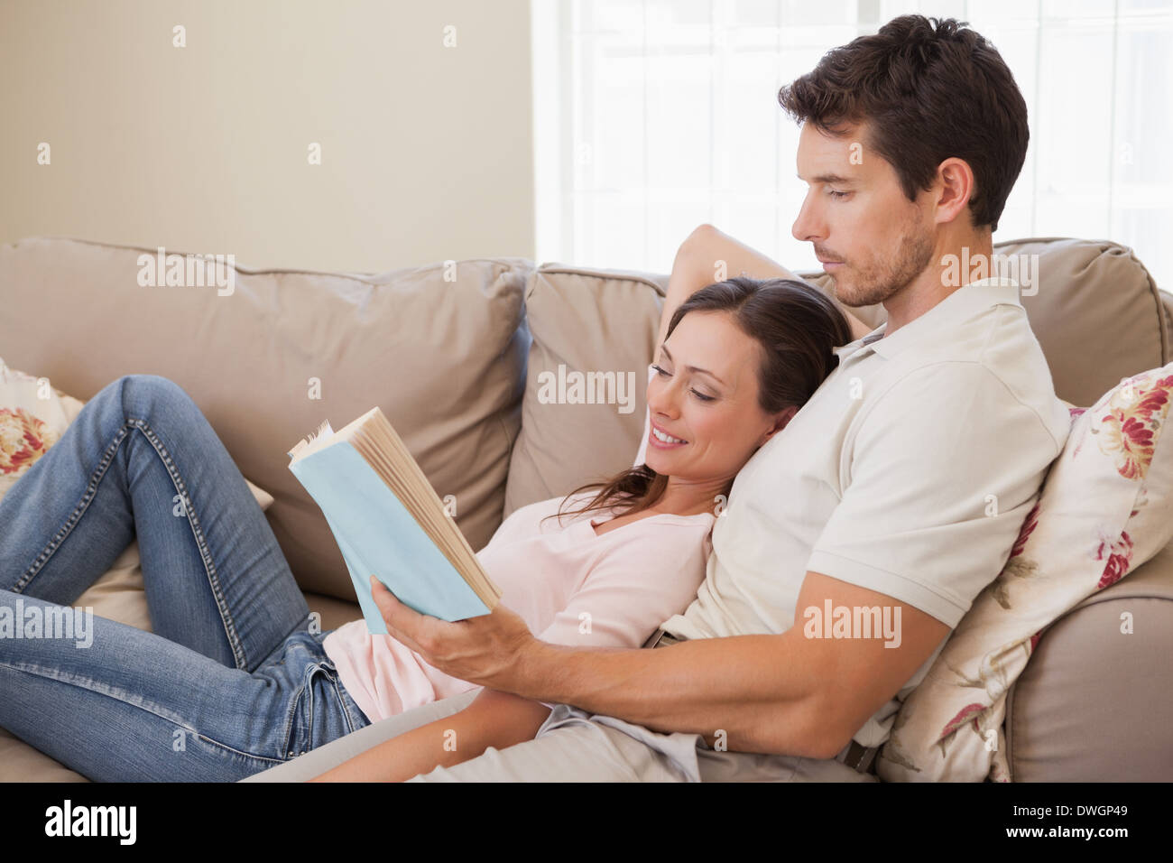 Relaxed young couple reading book on couch Stock Photo - Alamy