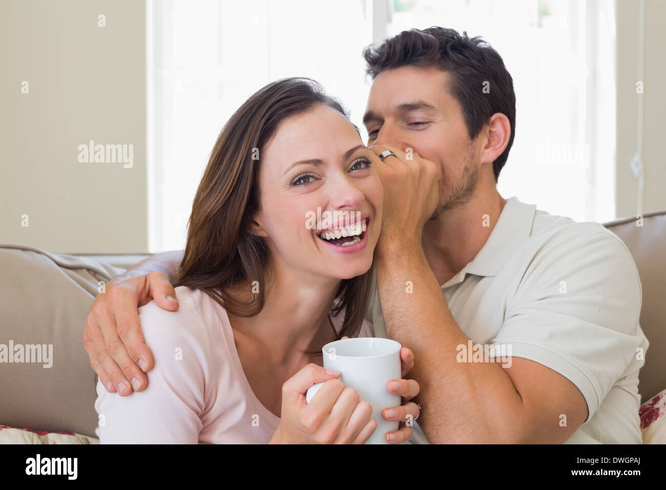 Man whispering secret into a cheerful womans ear in living room Stock ...
