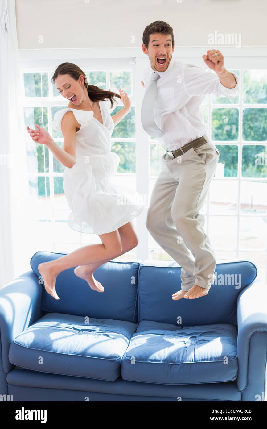 Cheerful young couple jumping on couch Stock Photo - Alamy