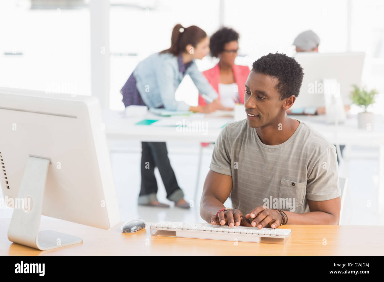 Male artist using computer with colleagues in background at office ...