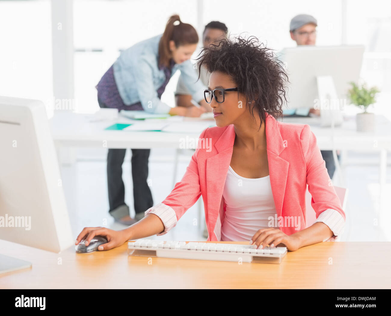Female artist using computer with colleagues in background at office ...