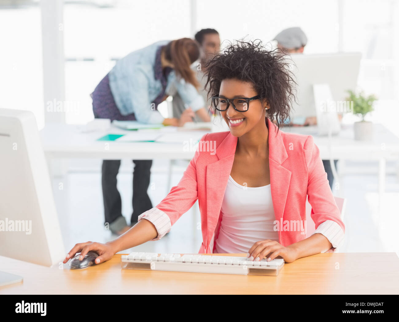 Female artist using computer with colleagues in background at office ...
