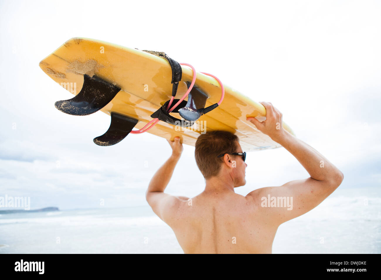 Male surfer resting surfboard on head at beach while looking towards ...