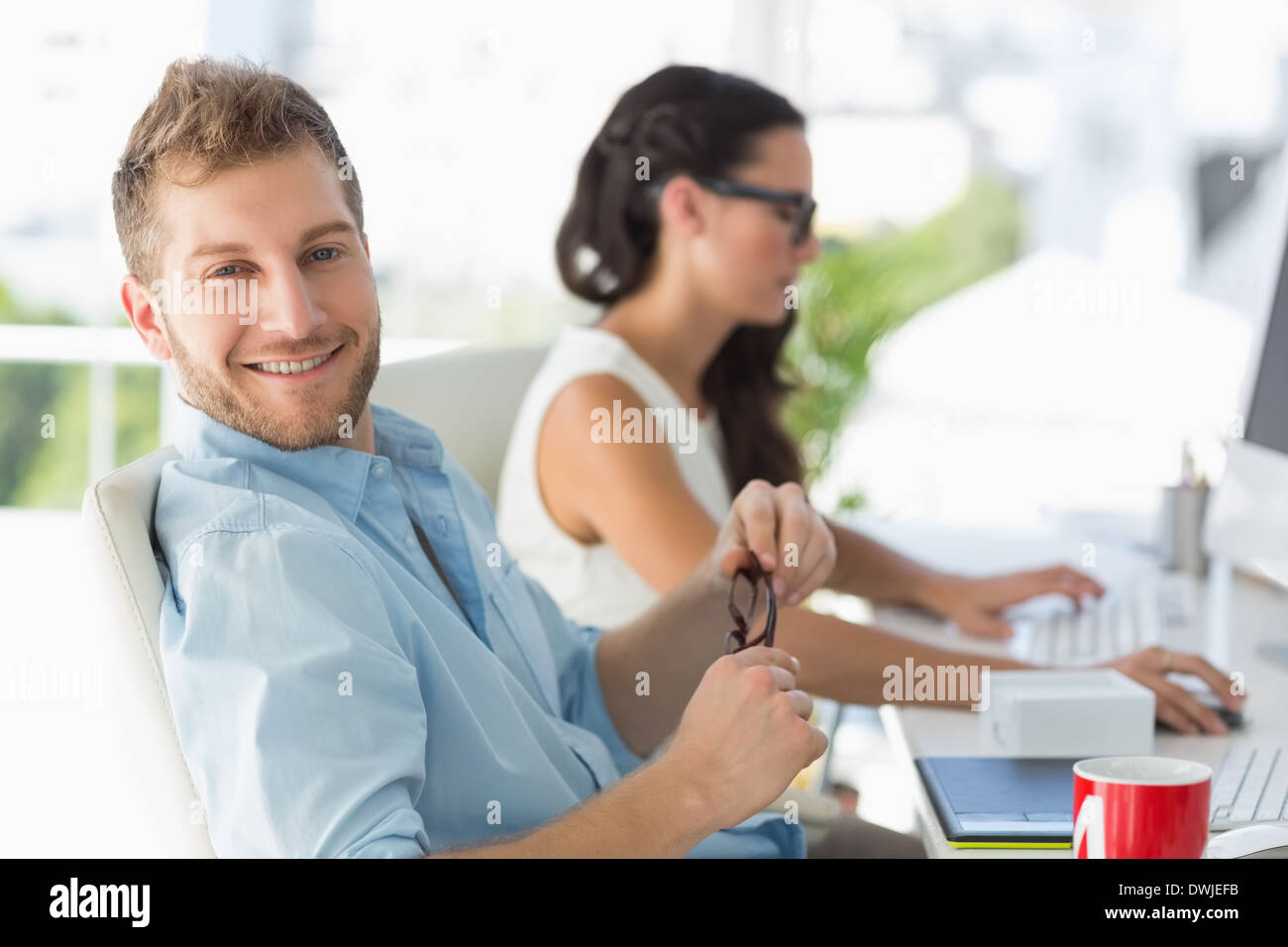 Attractive designer smiling at camera at desk Stock Photo - Alamy
