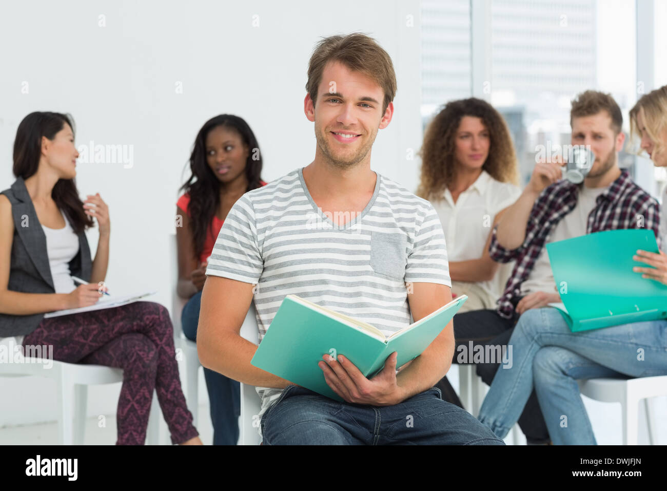 Smiling man taking notes while colleagues are talking behind him Stock ...