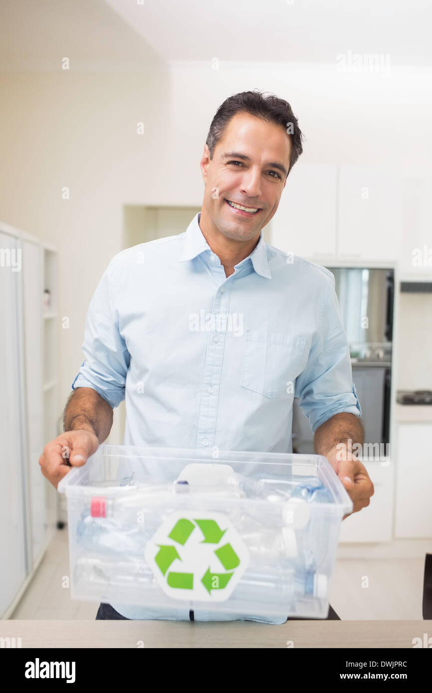 Portrait of a smiling man carrying recycling container in the kitchen ...