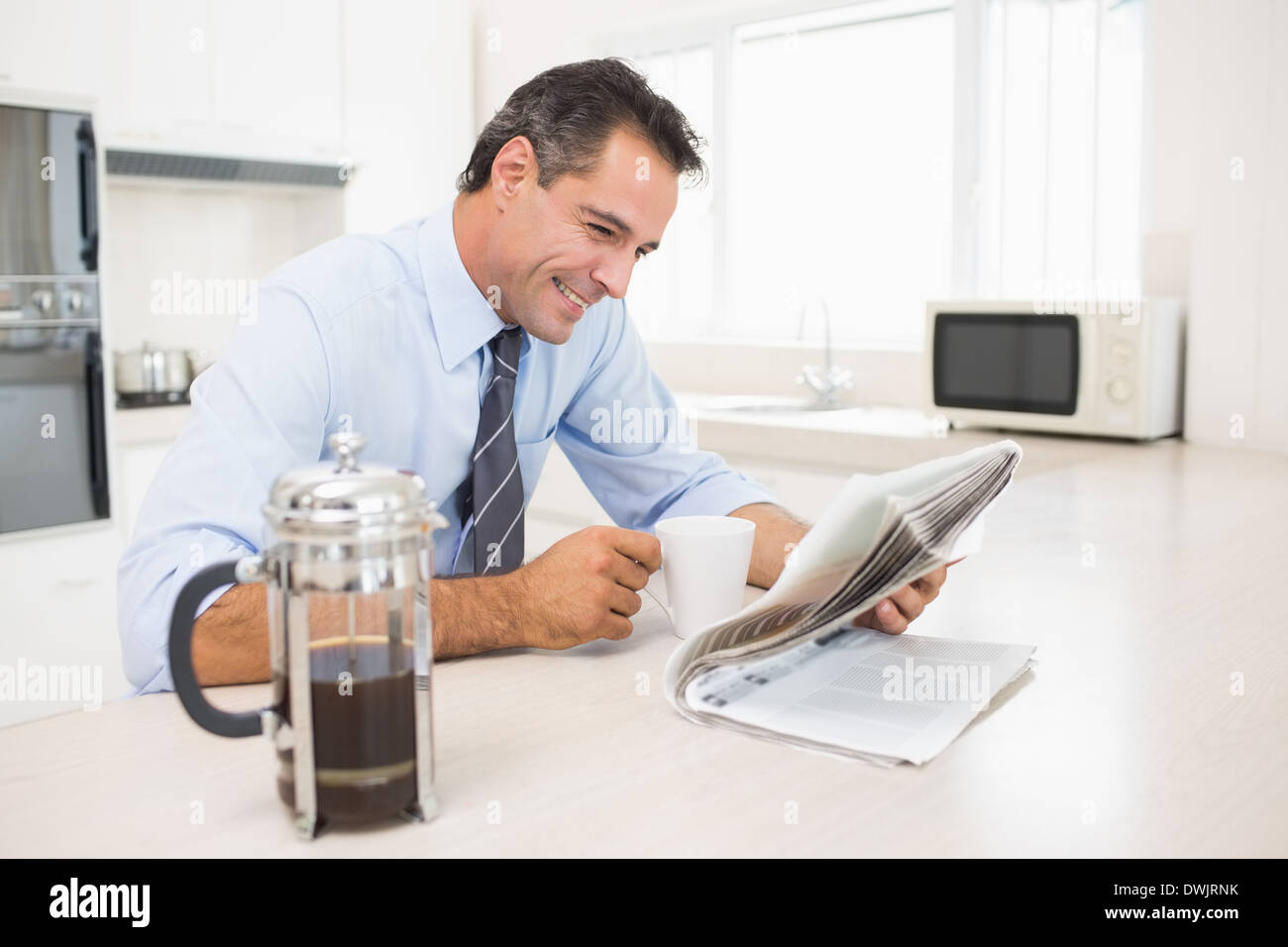 Smiling well dressed man with coffee cup reading newspaper in kitchen ...
