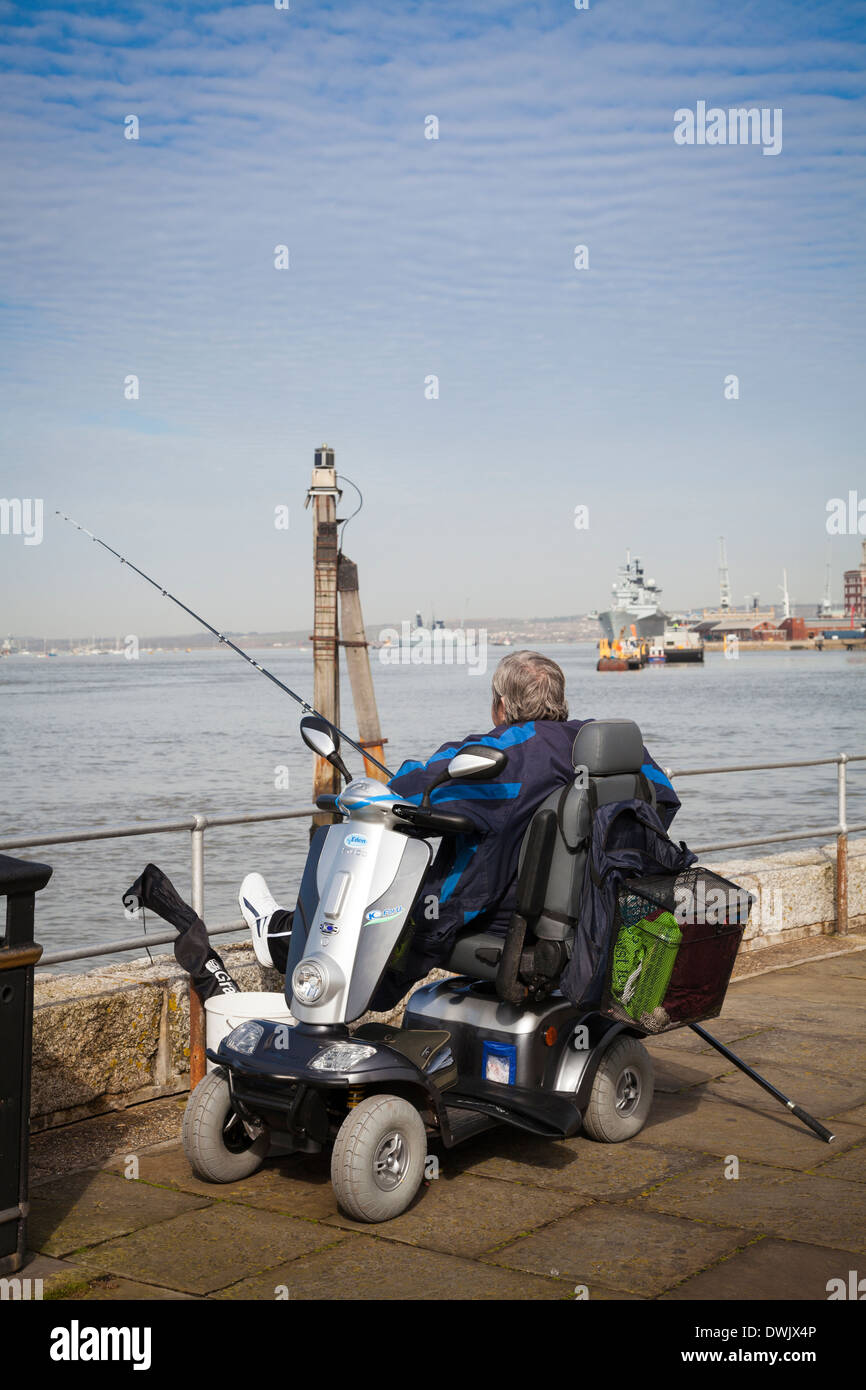 Man fishing at Portsmouth Harbour from Powered disability scooter Stock ...
