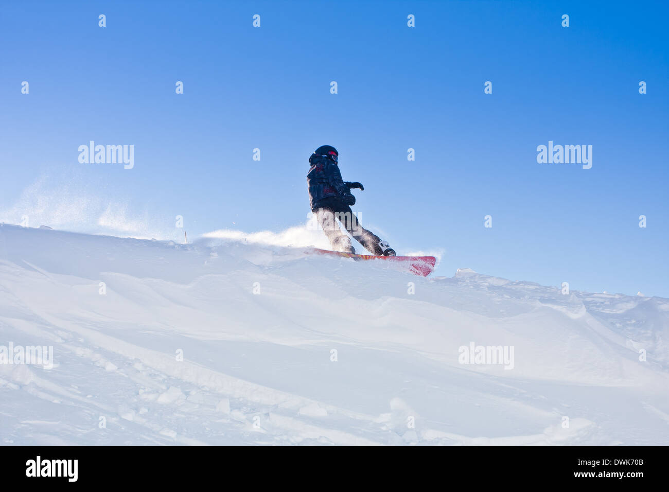 Young teenager riding a snowboard downhill under a clear blue sky and ...