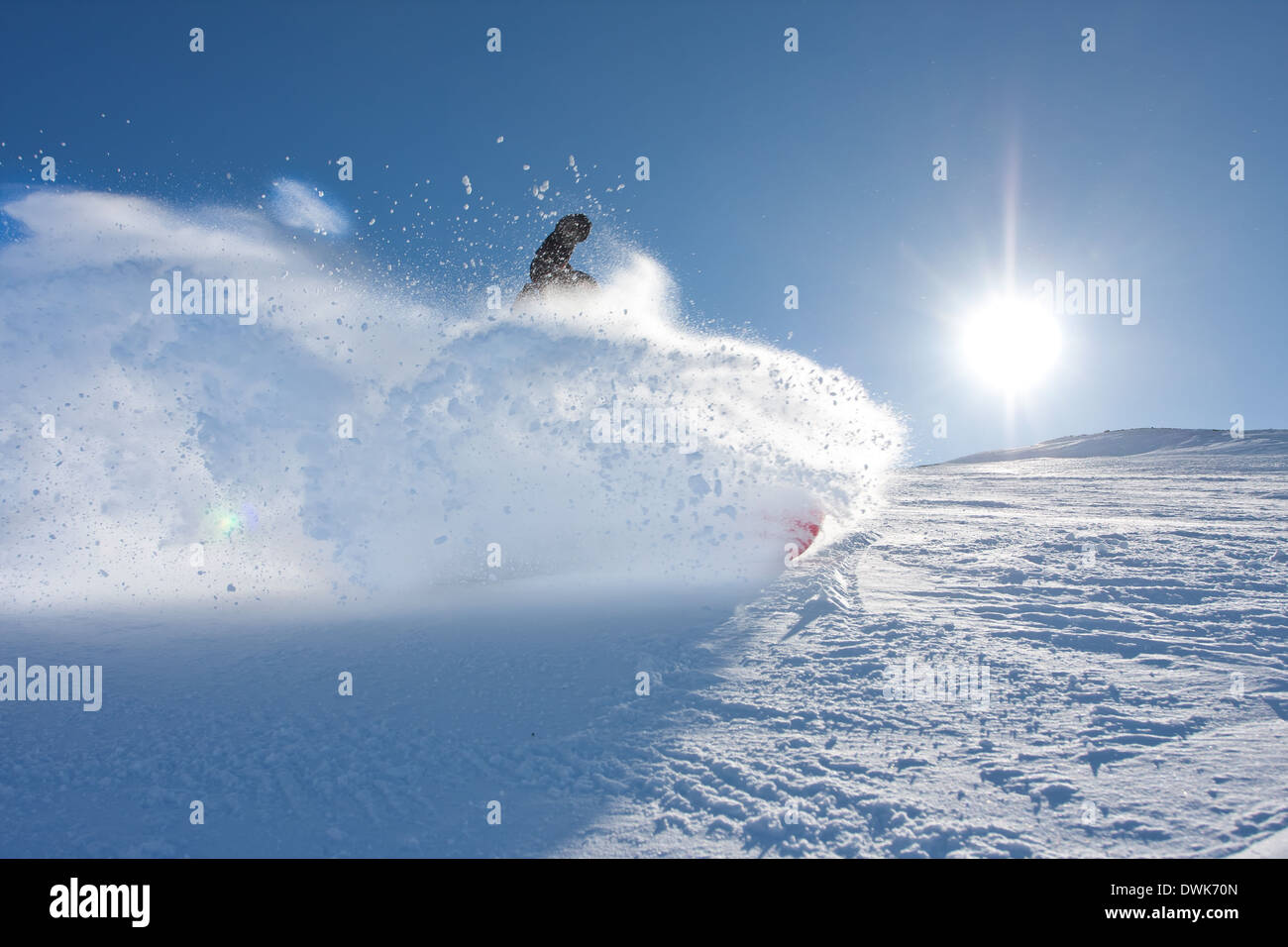 Young teenager riding a snowboard downhill under a clear blue sky and ...