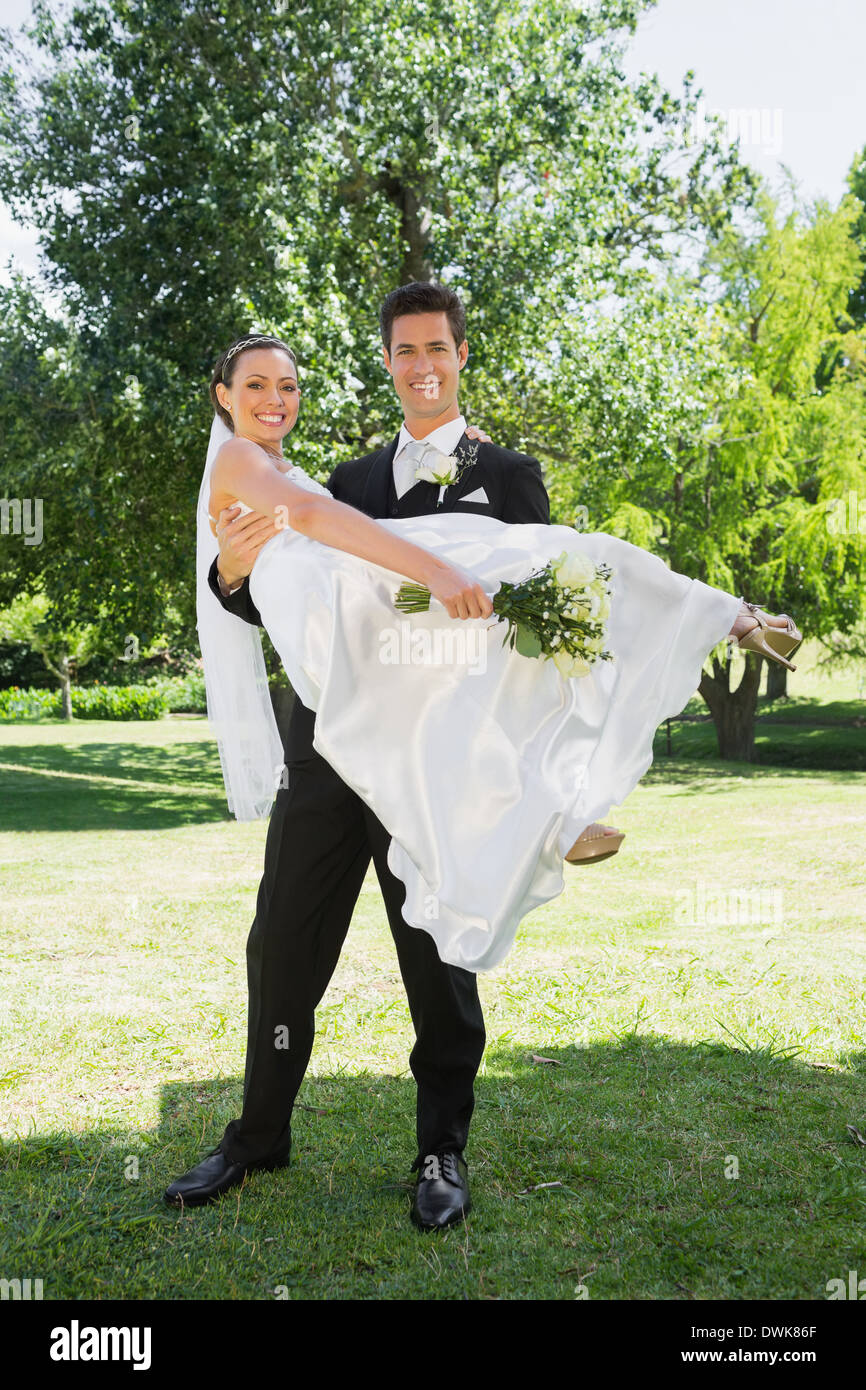 Happy groom lifting bride in arms at garden Stock Photo - Alamy
