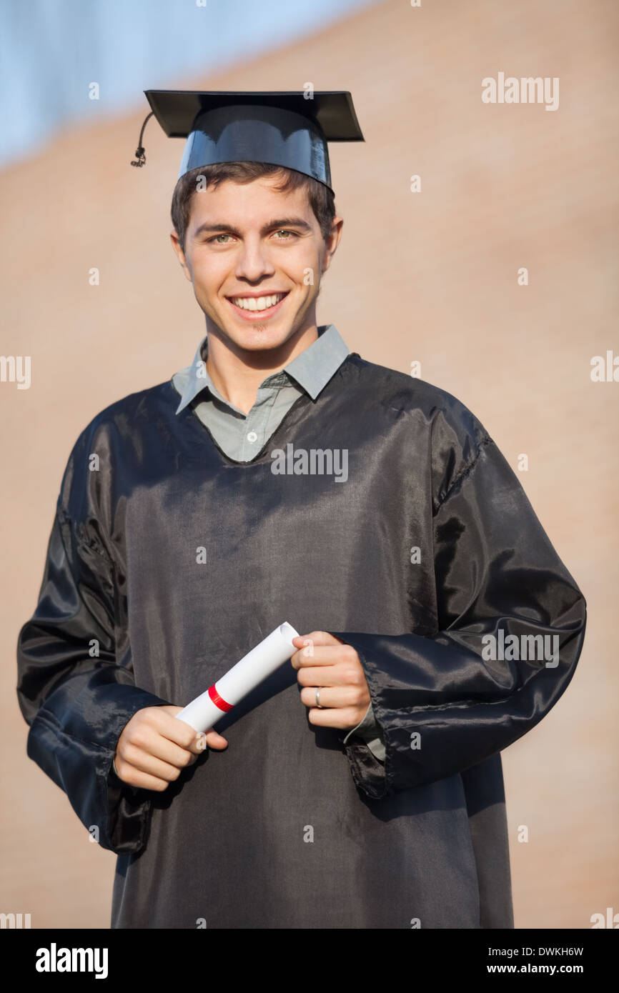 Happy Man In Graduation Gown Holding Certificate On Campus Stock Photo ...