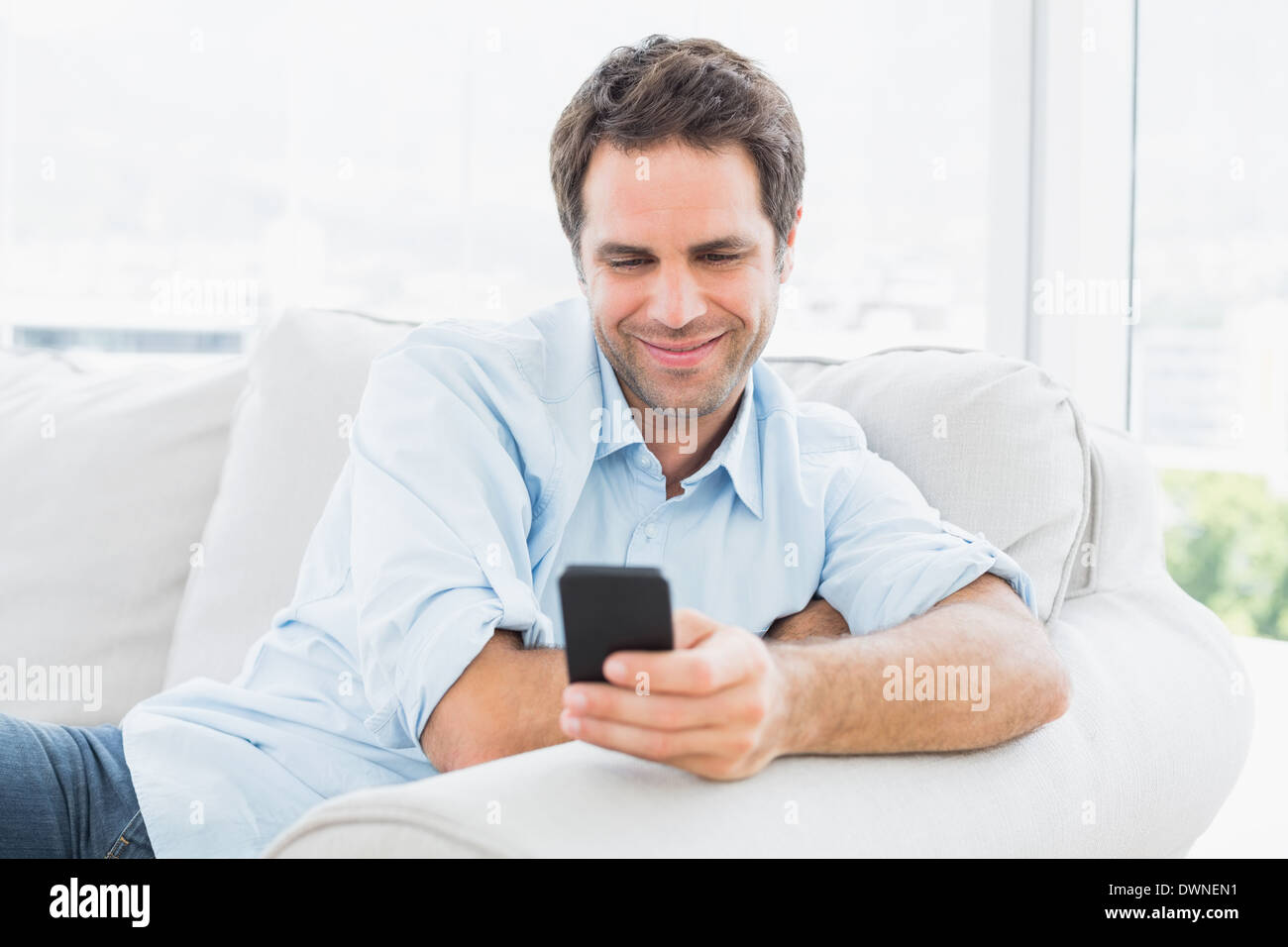 Happy man sitting on the couch sending a text Stock Photo - Alamy