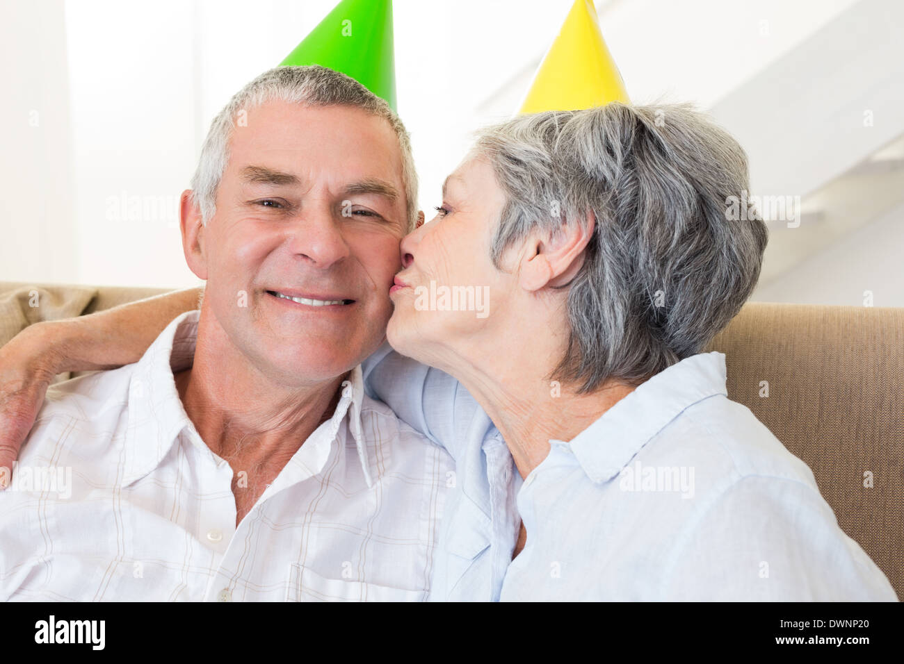 Senior couple sitting on couch wearing party hats Stock Photo - Alamy