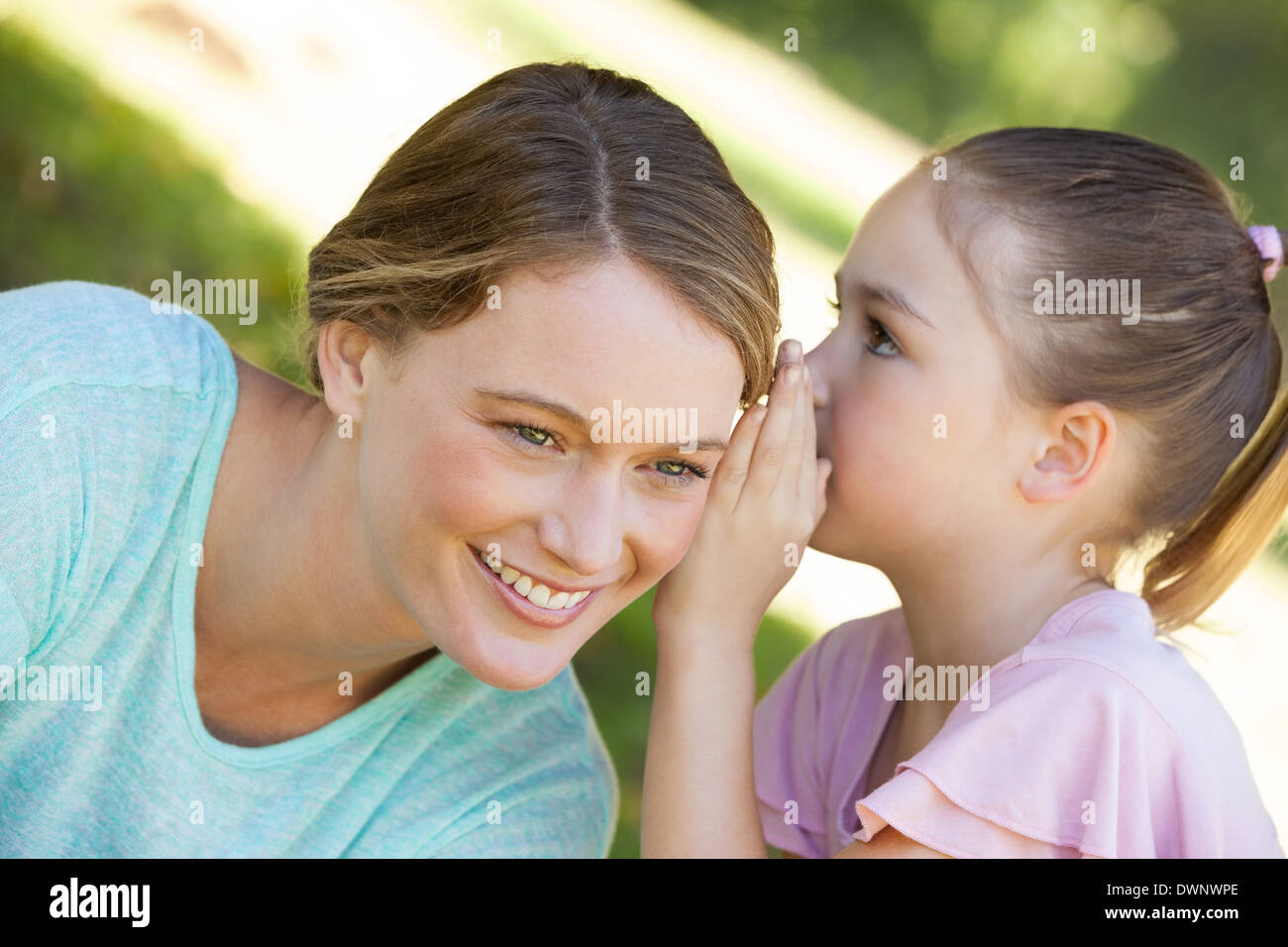 Girl whispering secret into mother's ear at park Stock Photo - Alamy