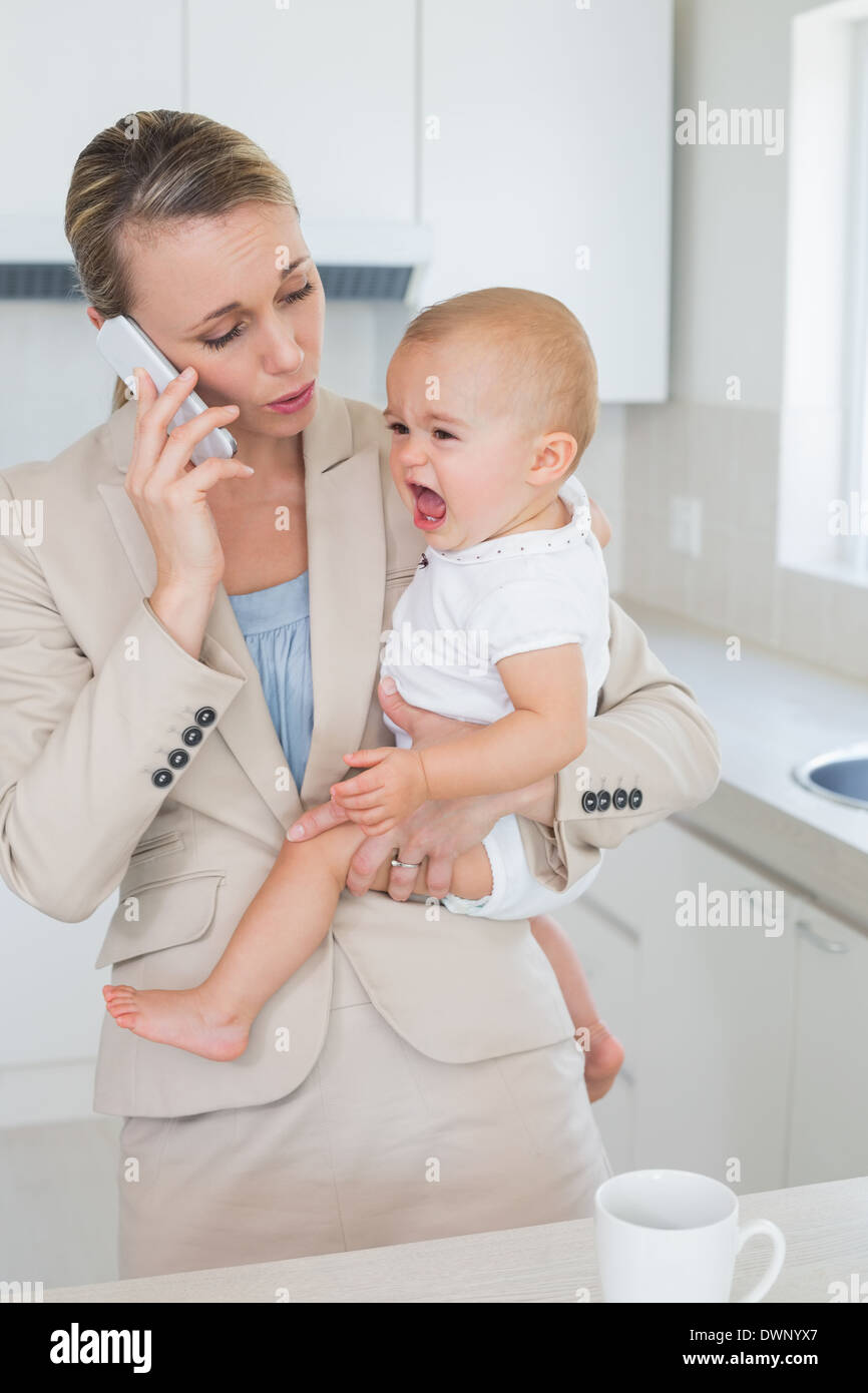 Businesswoman holding her crying baby talking on the phone Stock Photo ...