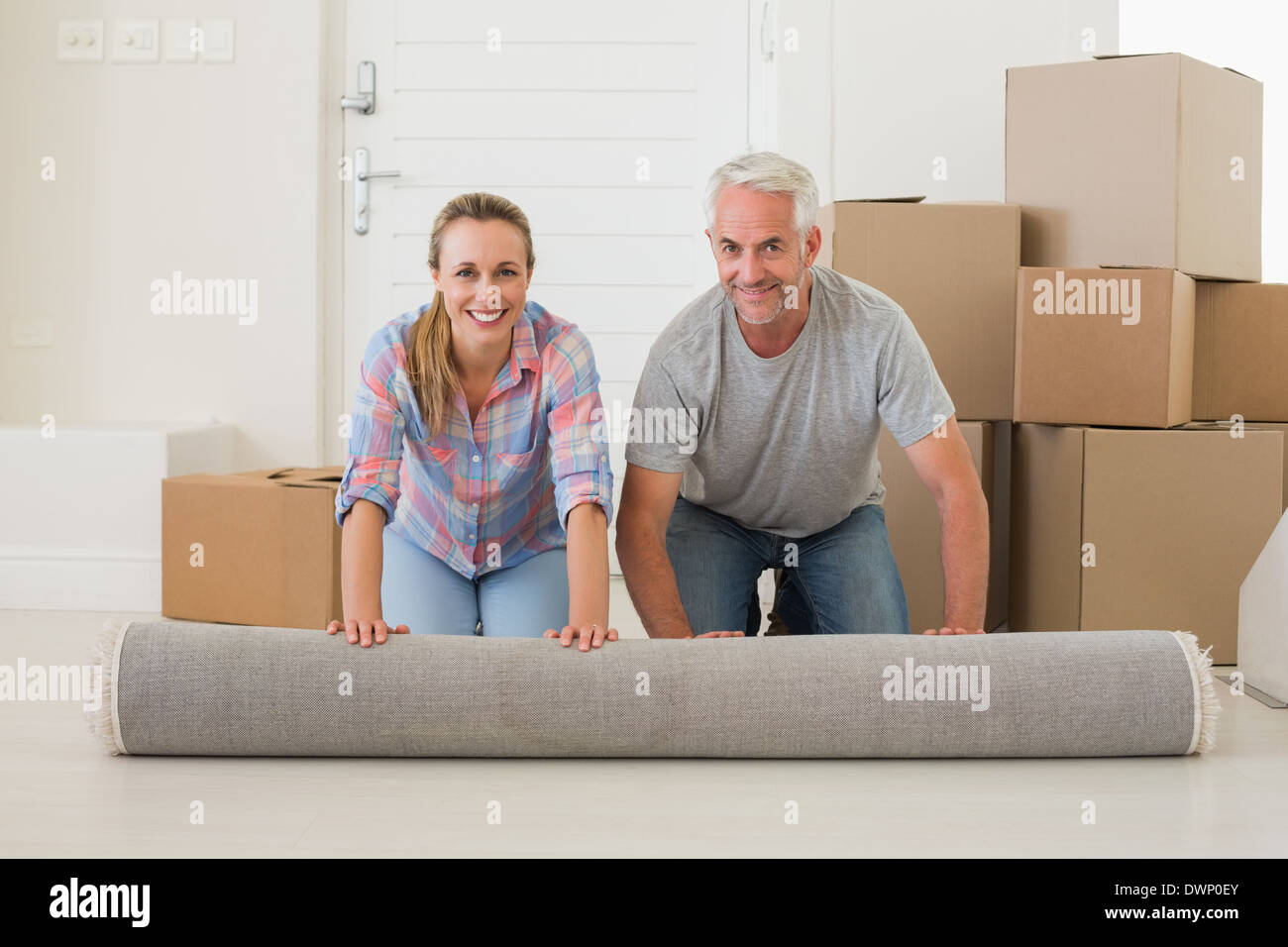 Happy couple rolling out new rug Stock Photo - Alamy