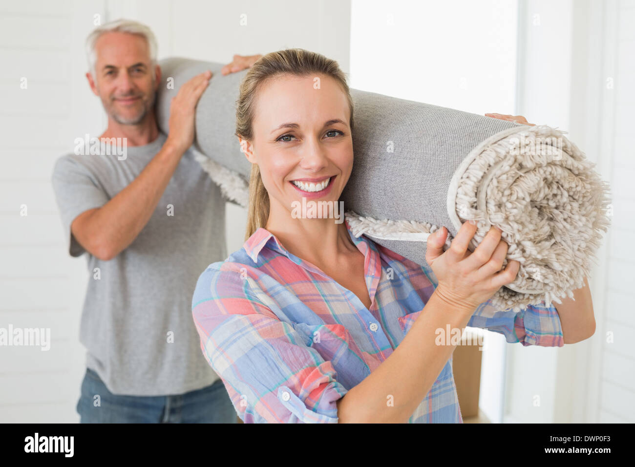 Happy couple carrying a rolled up rug together Stock Photo - Alamy