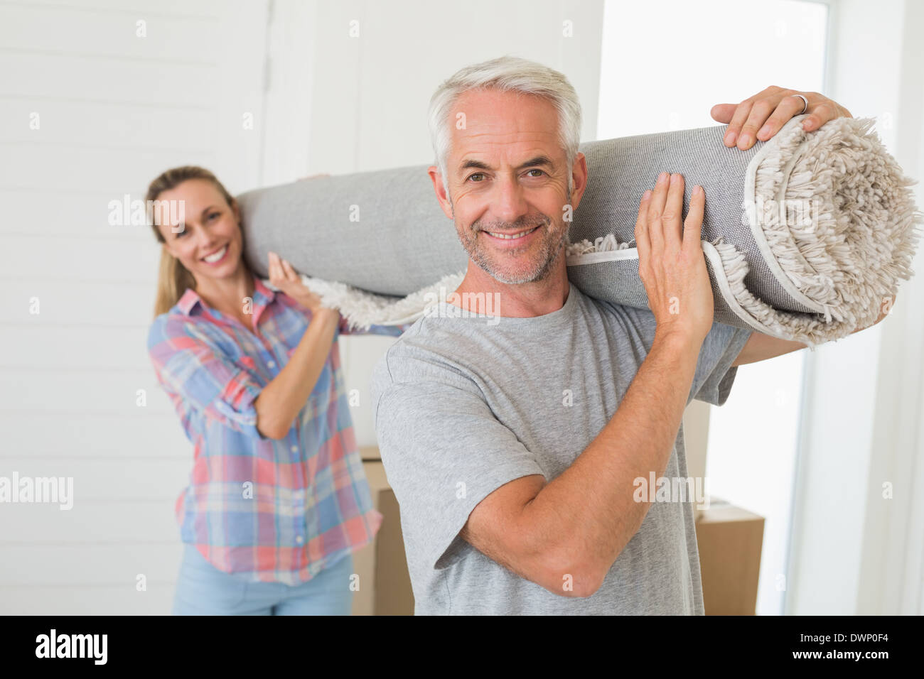 Happy couple carrying a rolled up rug together Stock Photo - Alamy