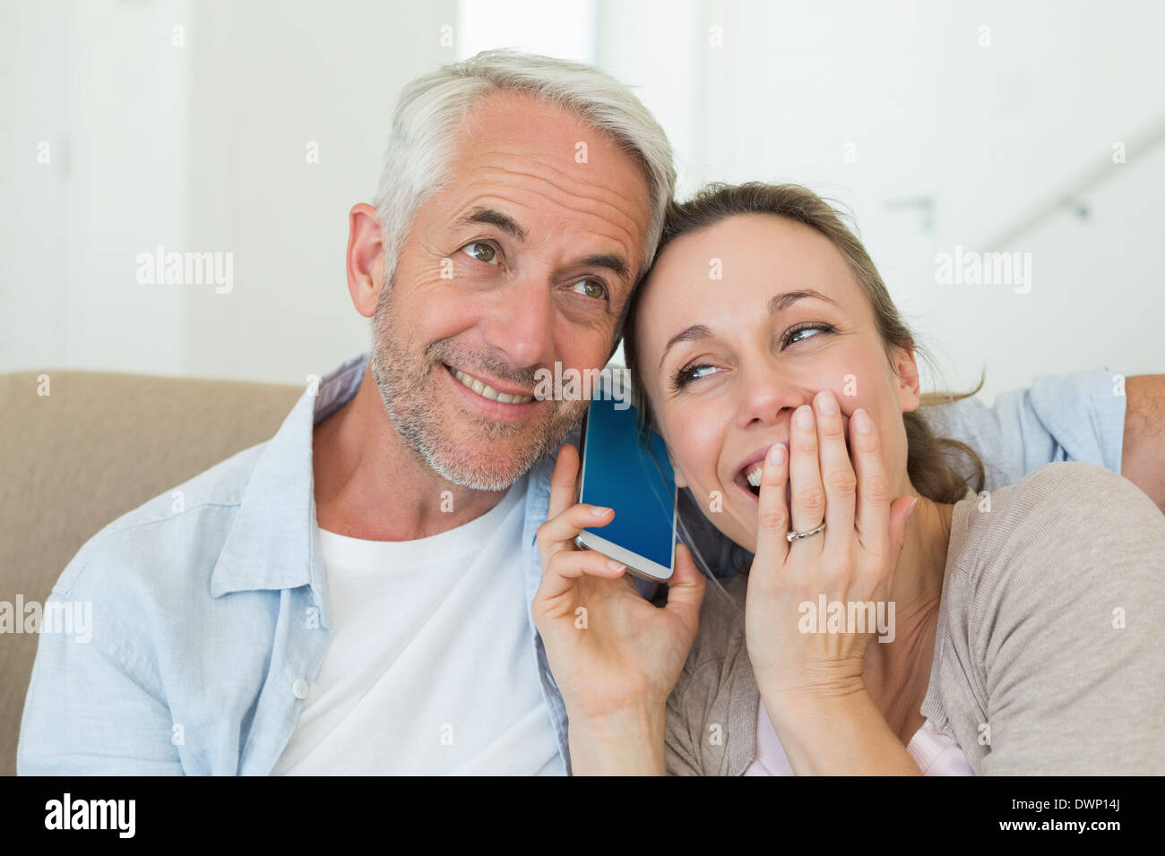 Happy couple listening to phone call together on the couch Stock Photo ...
