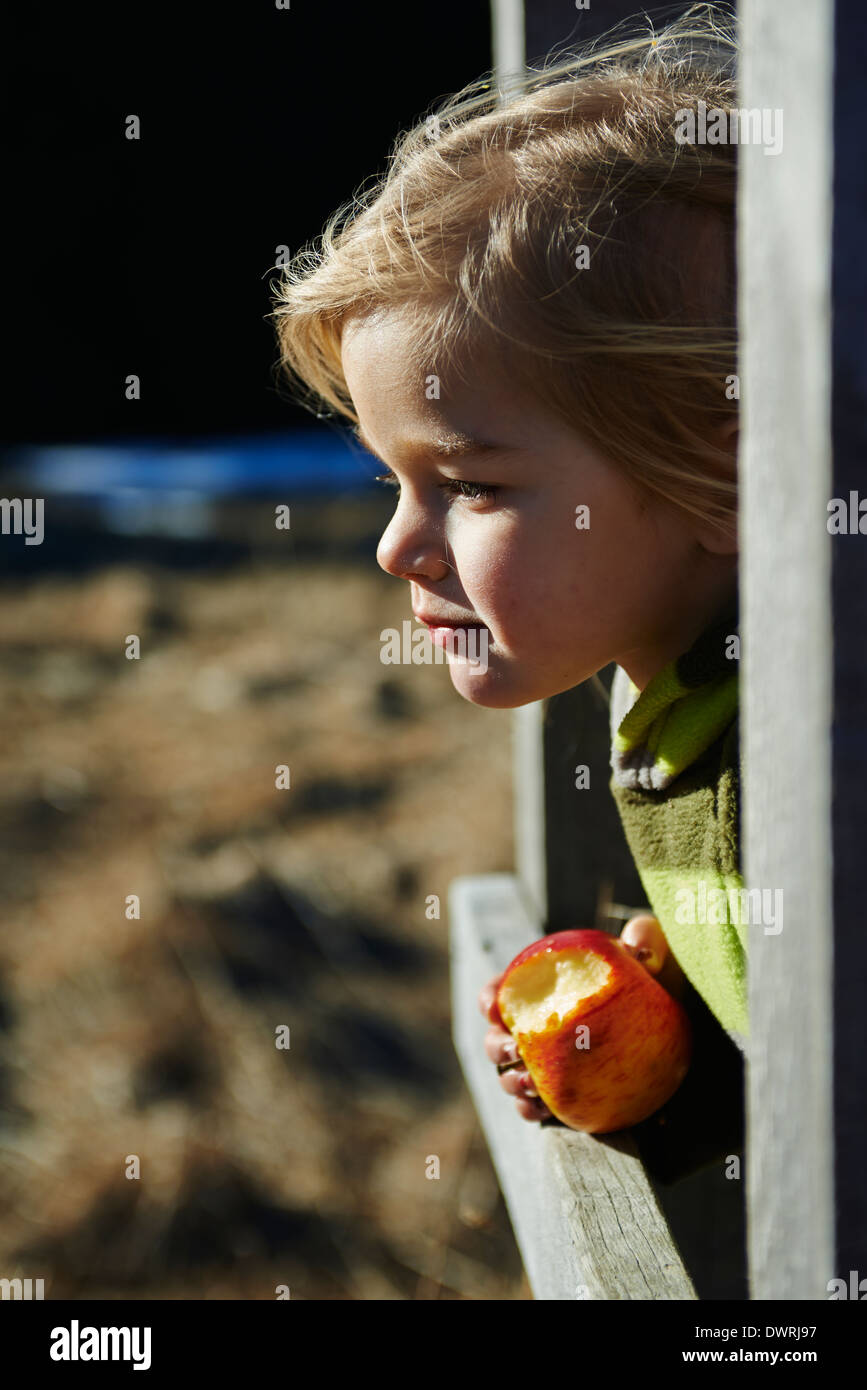Little blond child girl side face portrait eating apple in wooden ...