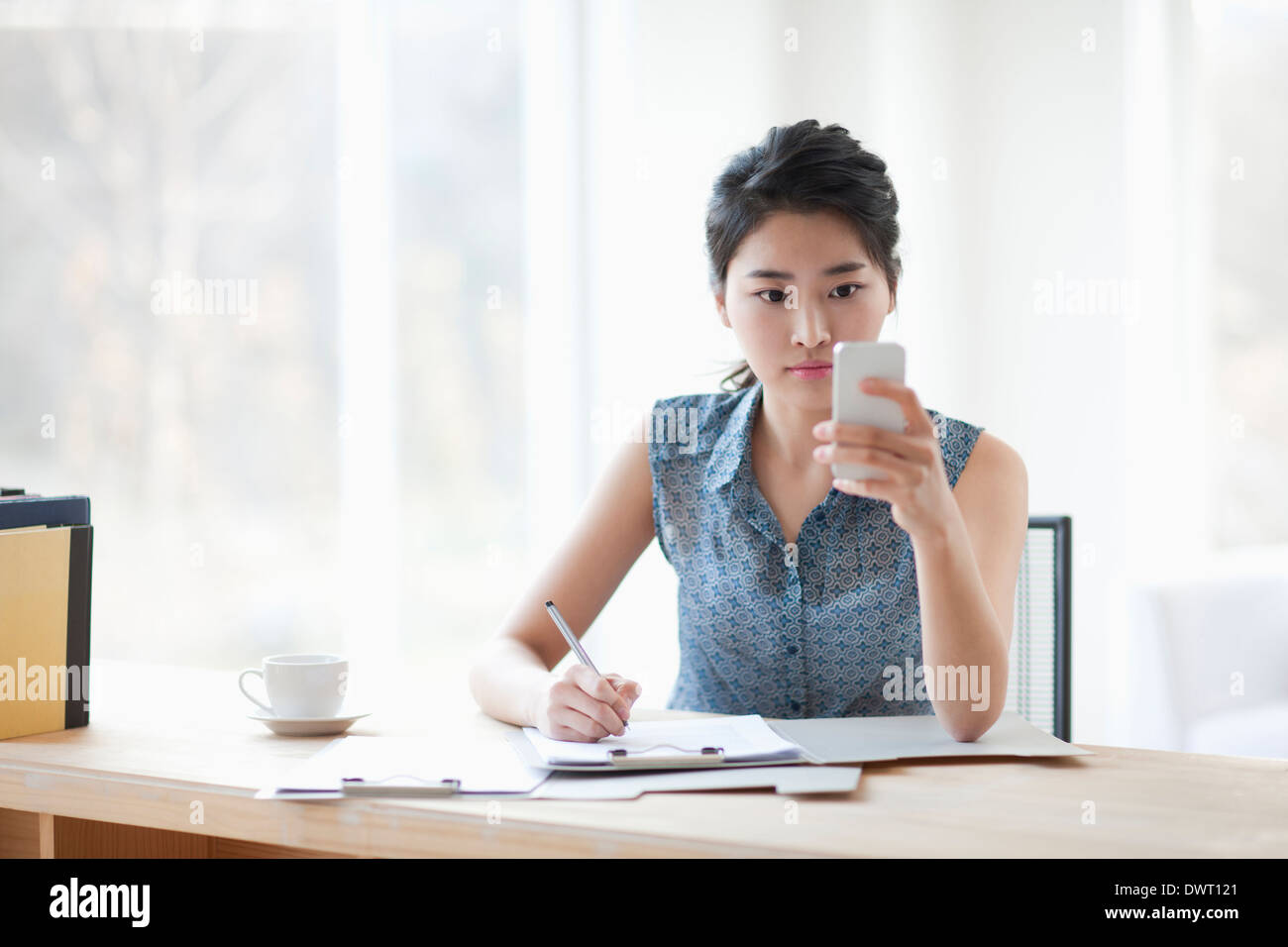 a woman sitting at desk writing something Stock Photo - Alamy