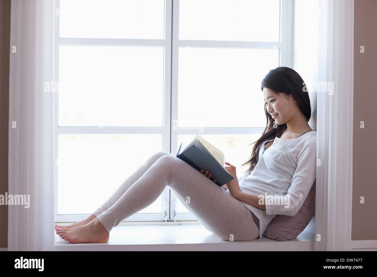 a woman leaning on window and reading a book Stock Photo - Alamy
