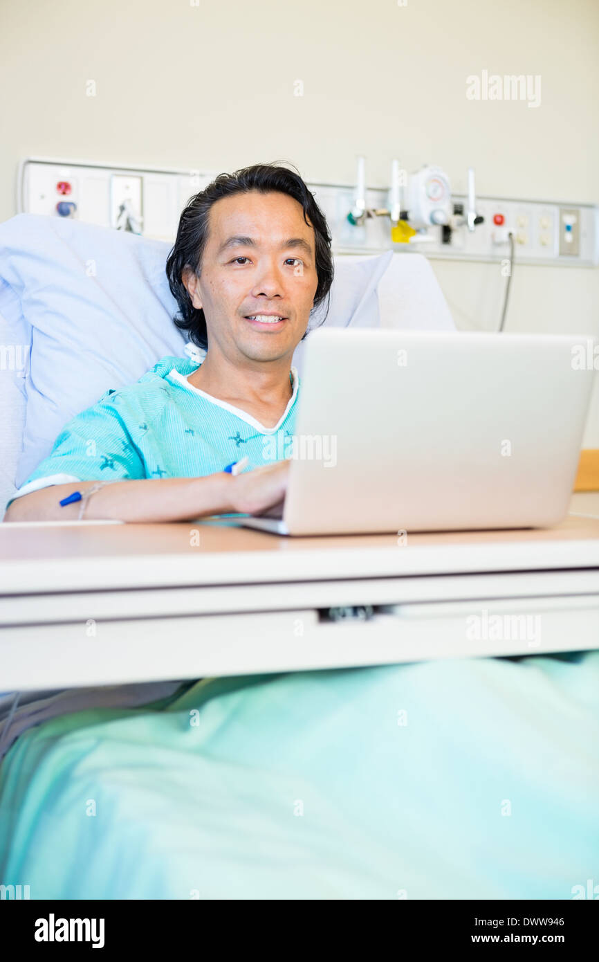 Happy Male Patient Using Laptop On Hospital Bed Stock Photo - Alamy