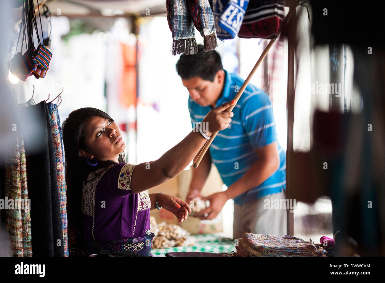 Tending to her stall a woman moves high hanging goods witha stick and ...