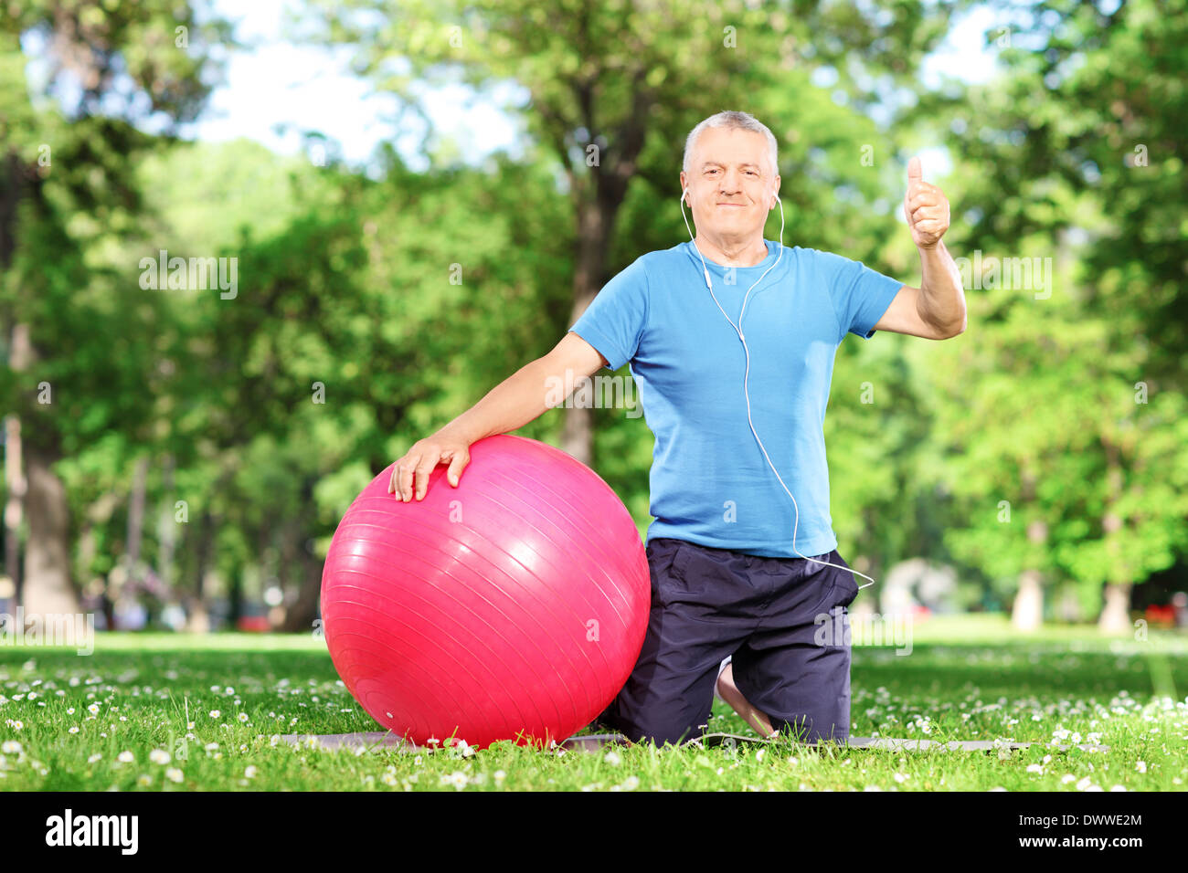 Healthy man giving thumb up seated on an exercise mat in a park Stock ...