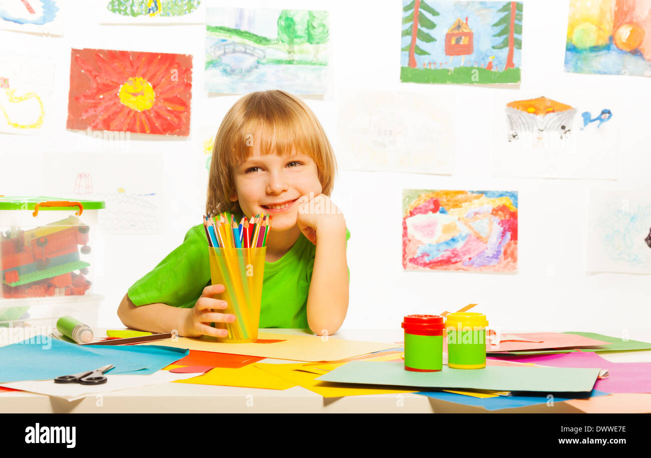 Happy smiling blond boy sitting on the table with pencils and color ...