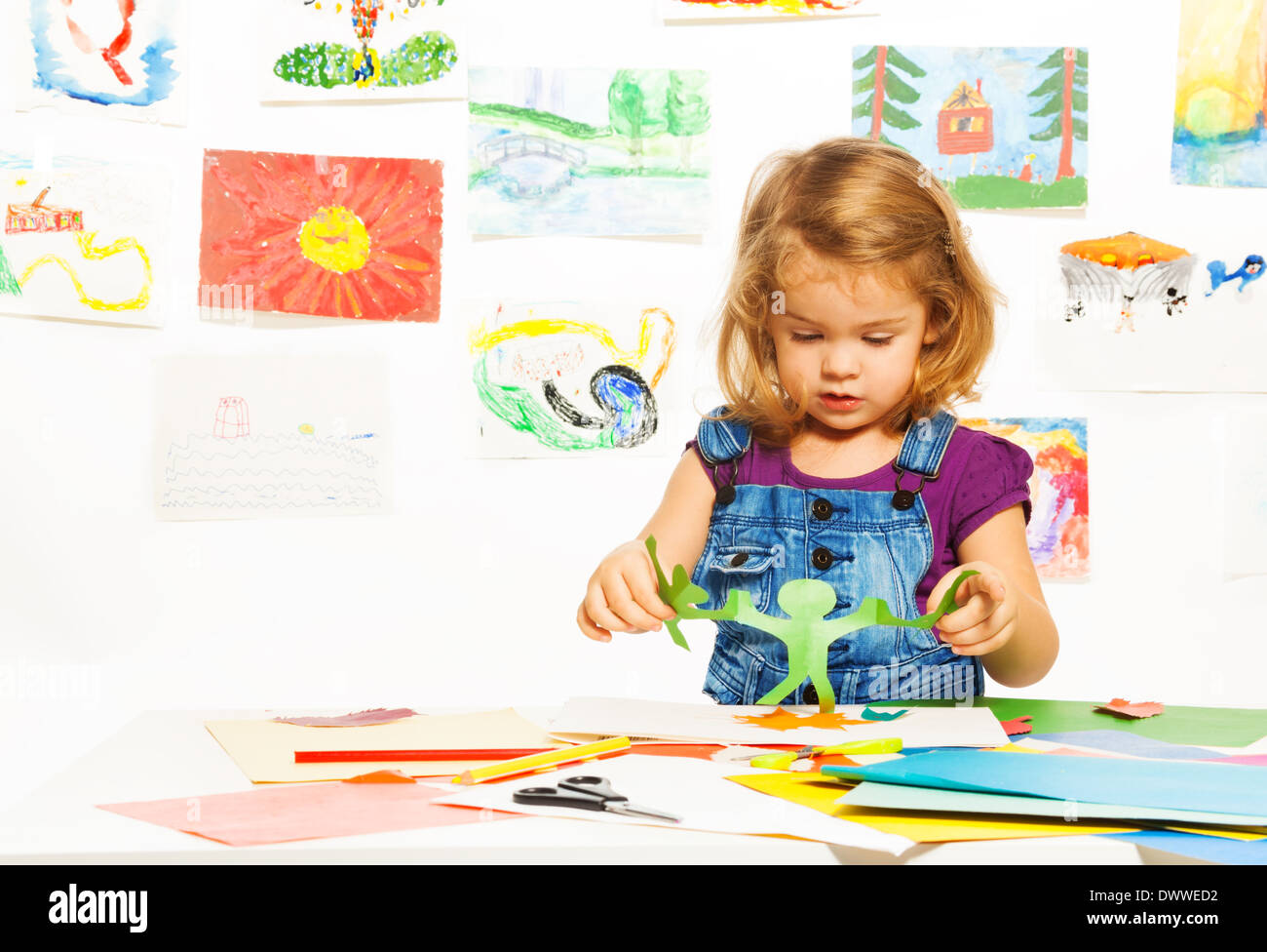 Little 3 years old blond girl gluing color cardboard holding cut out ...