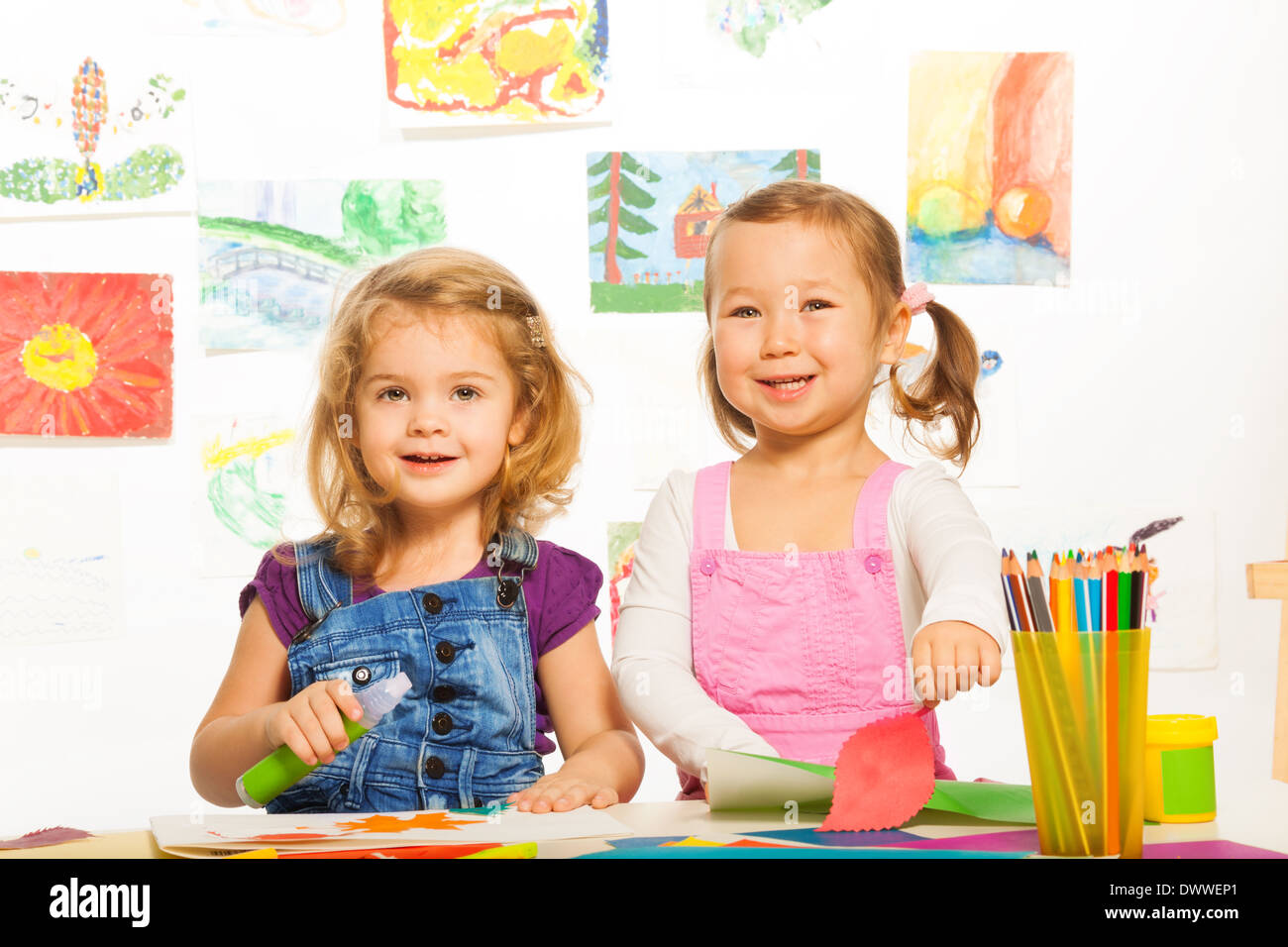 Two happy color little girls cutting and gluing with pictures on ...
