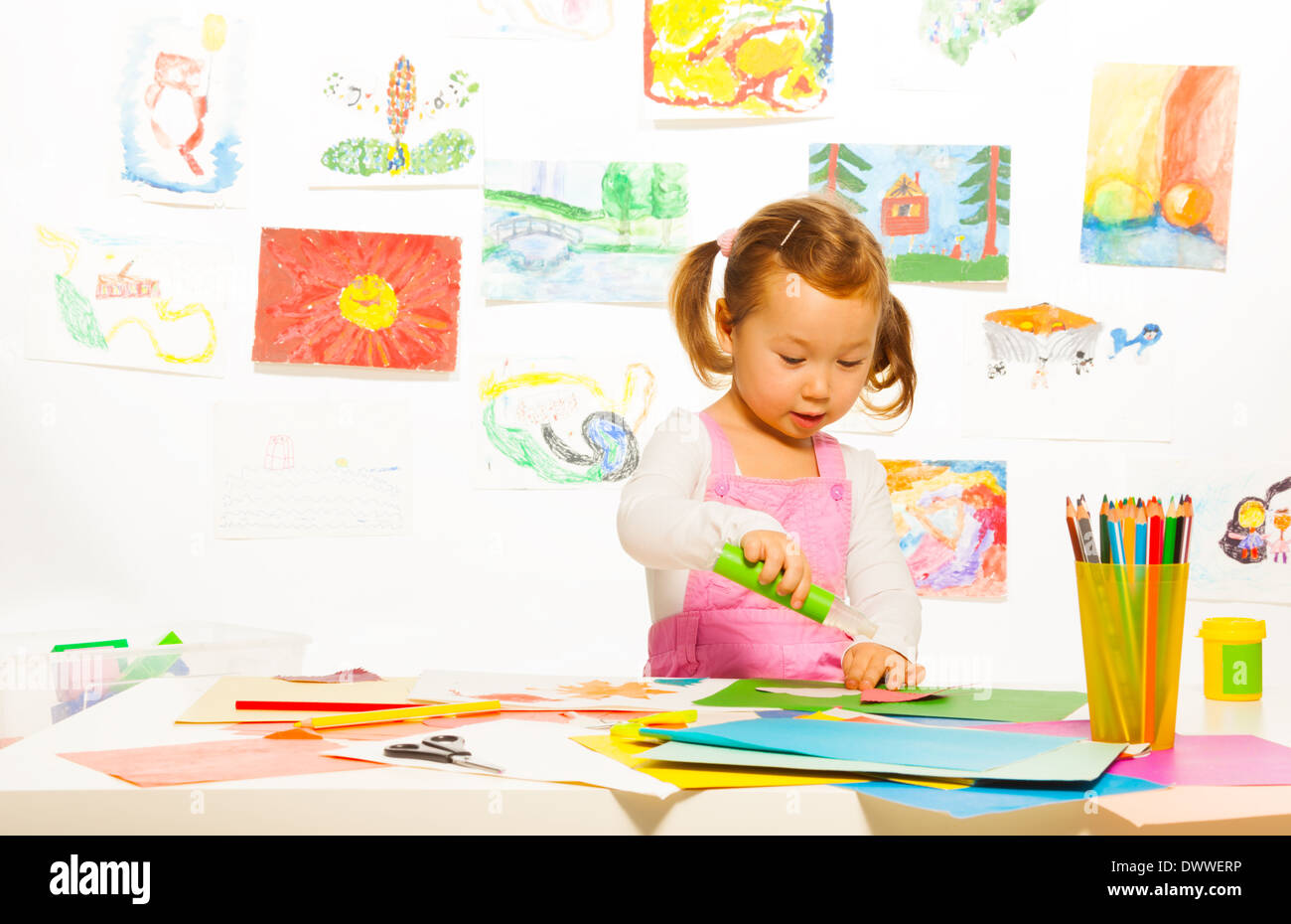 Little Asian girl gluing and making crafts with color cardboard paper ...
