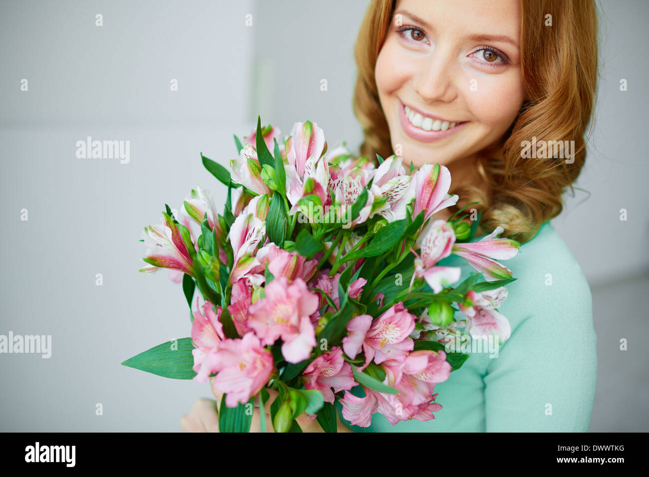 Portrait of smiling female with bunch of pink lilies looking at camera ...