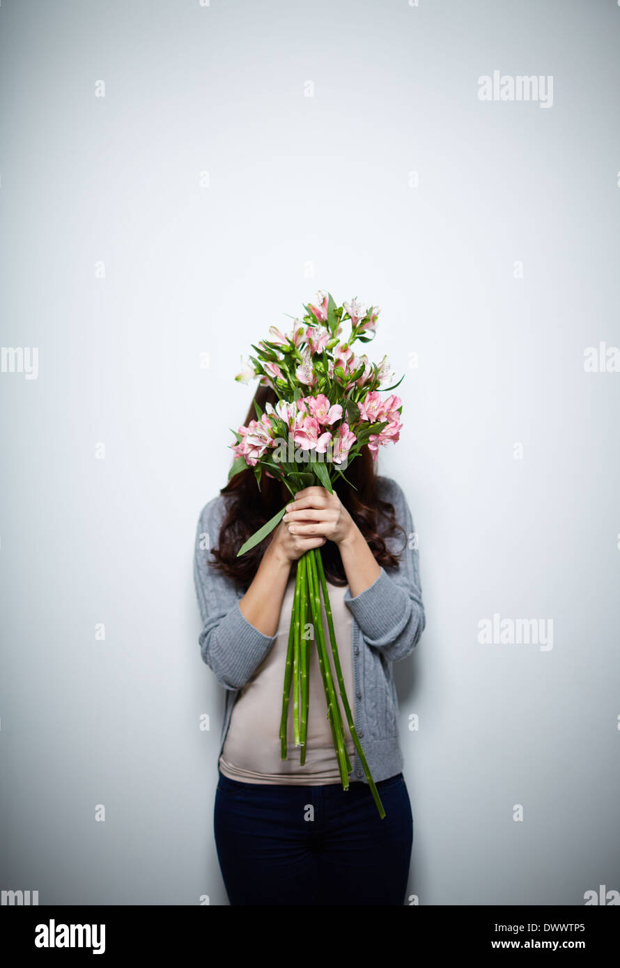 Portrait of young female hiding her face behind bunch of fresh flowers ...