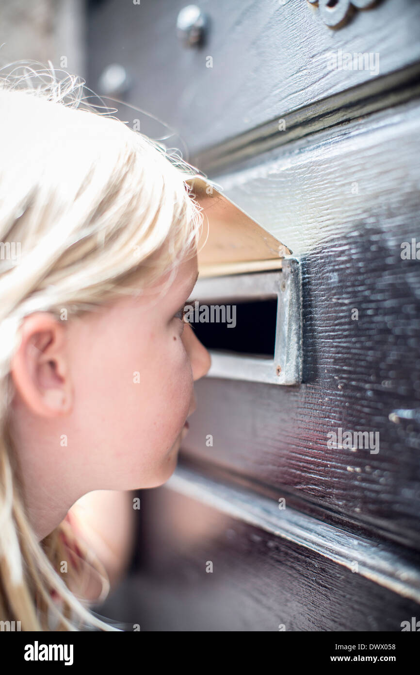 Side view of girl looking through mail slot in door Stock Photo - Alamy
