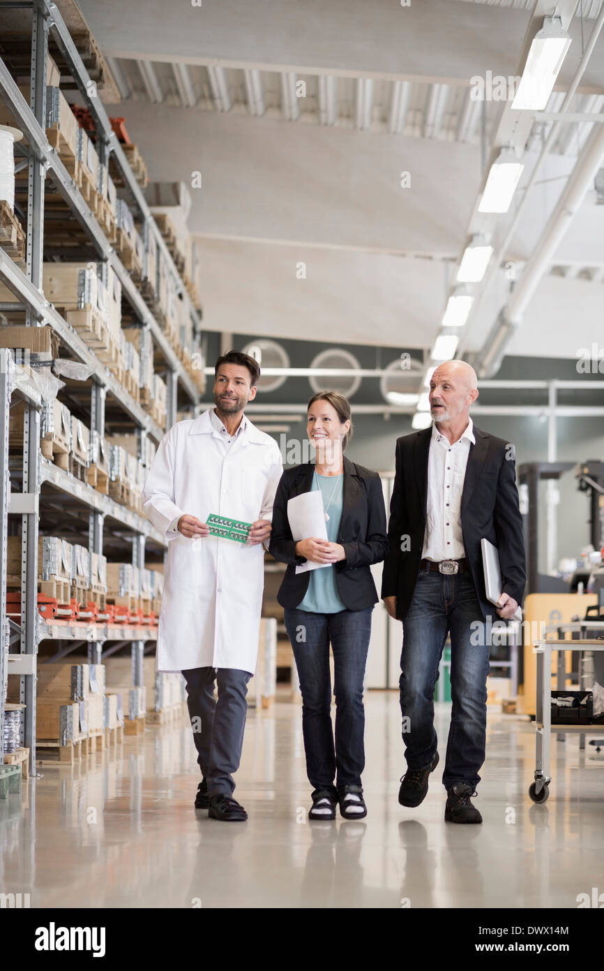 Full length of business people and engineer walking in manufacturing ...