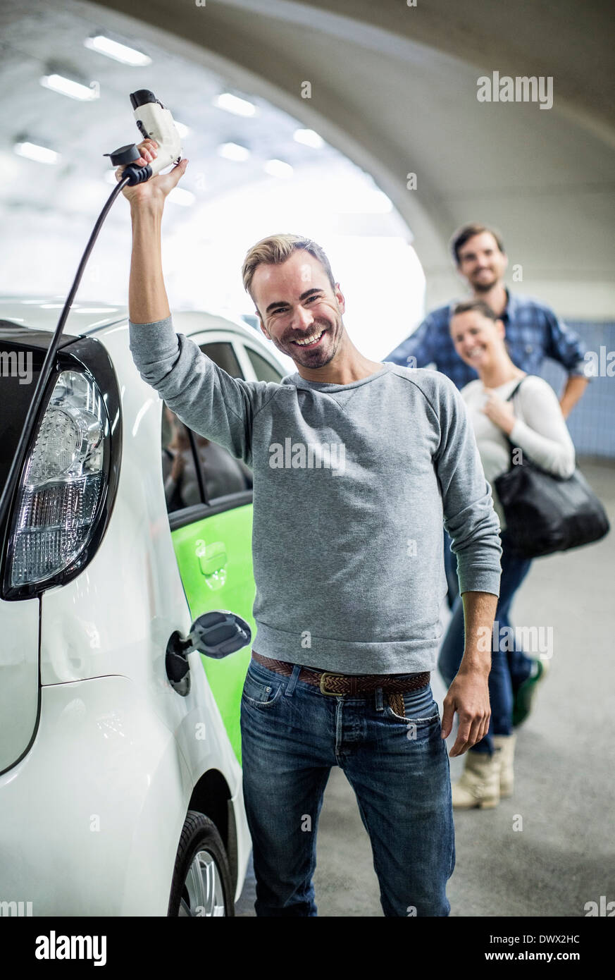 Portrait of happy man holding electrical charger with friends standing ...
