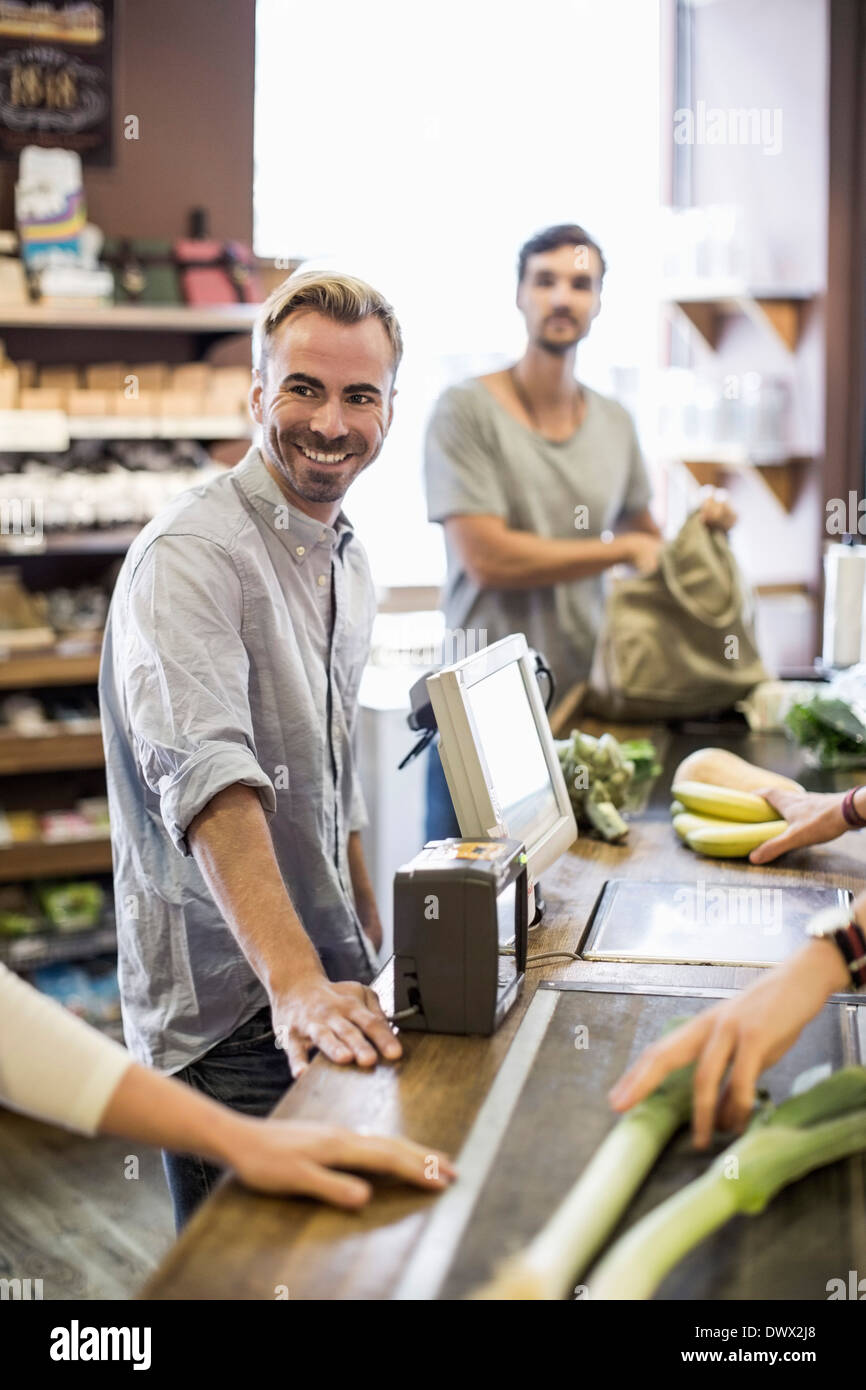 Smiling man standing at supermarket checkout counter with friend in ...