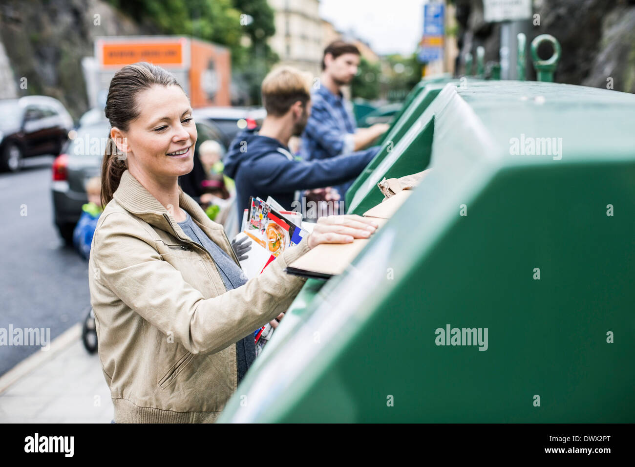 Woman and friends putting recyclable materials into recycling bins ...