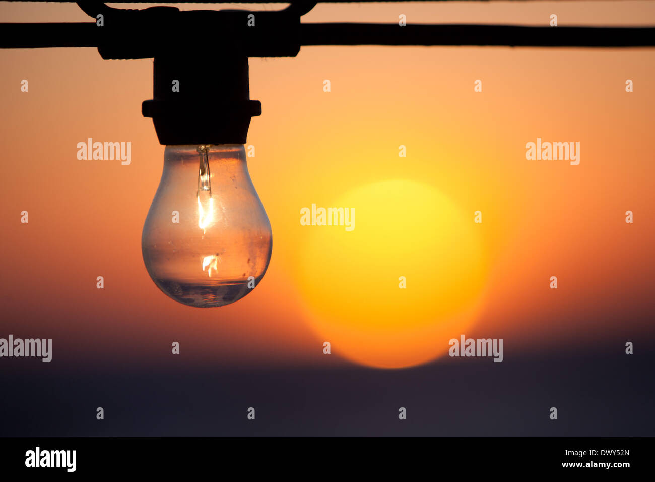 The filament wire of light bulb is barely visible against the sunset ...