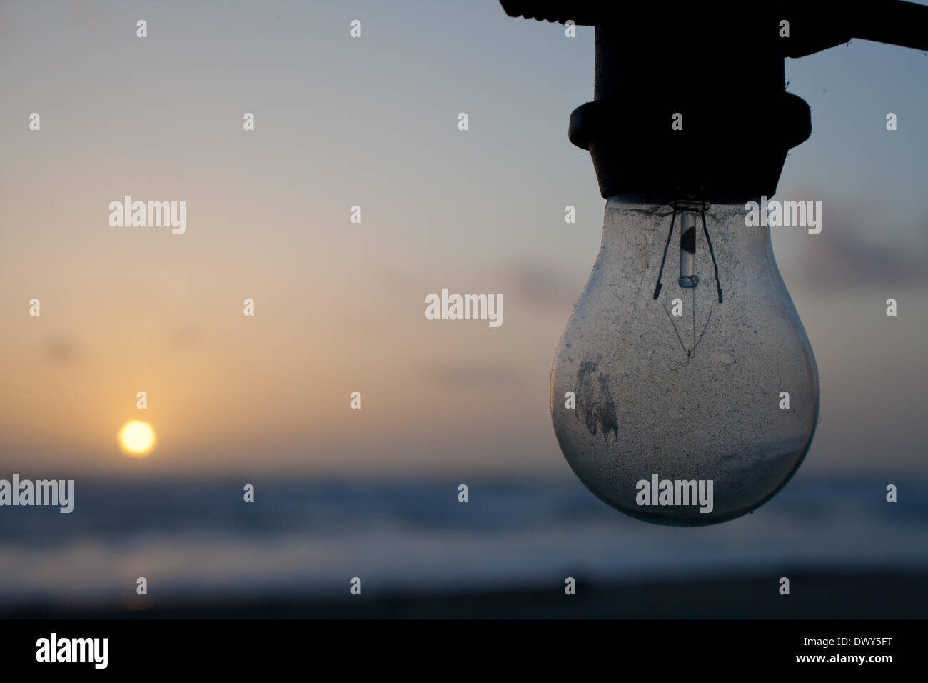 The filament wire of light bulb is barely visible against the sunset ...