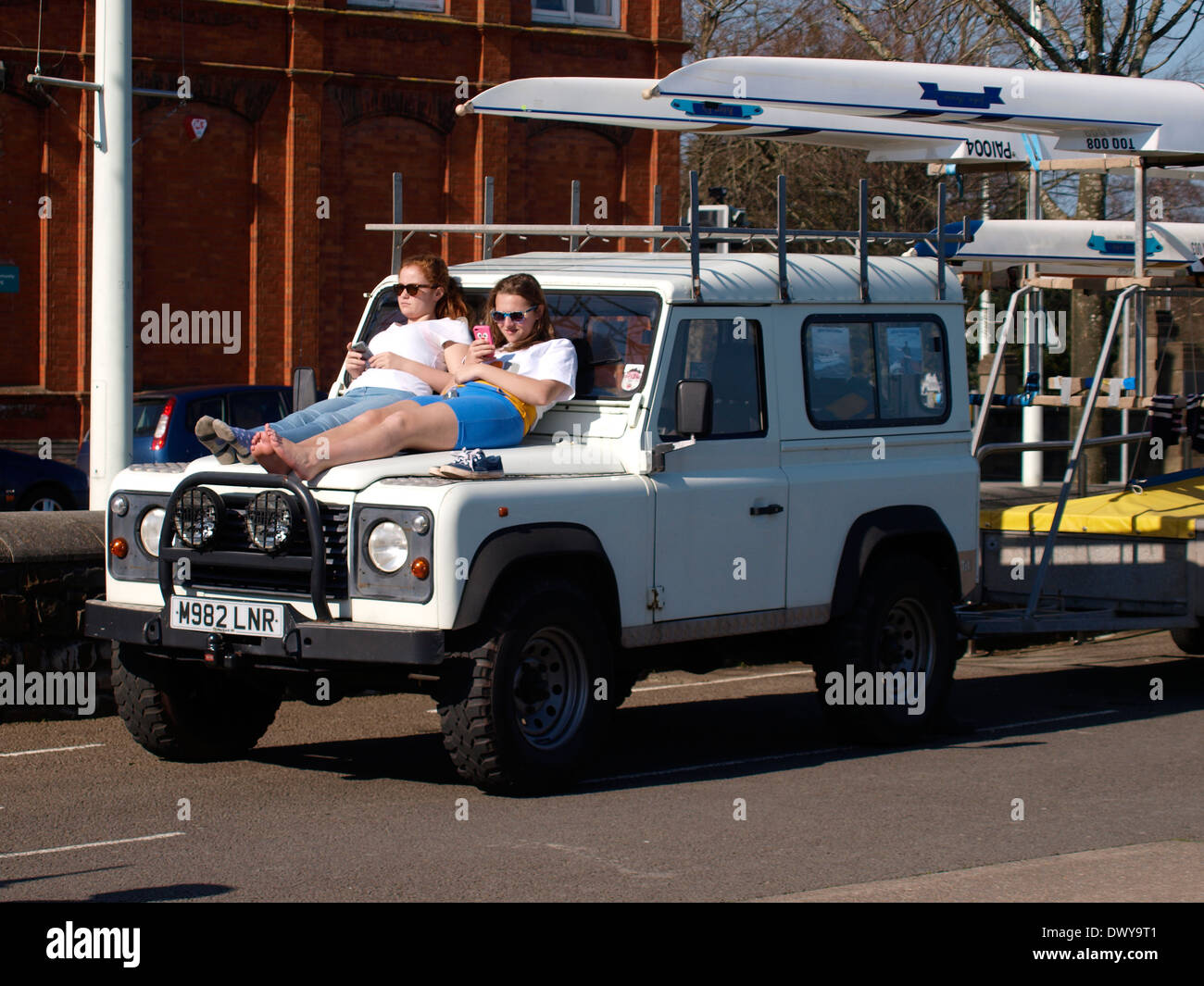 Two teenage girls sat on the bonnet of a Land Rover in the sunshine ...