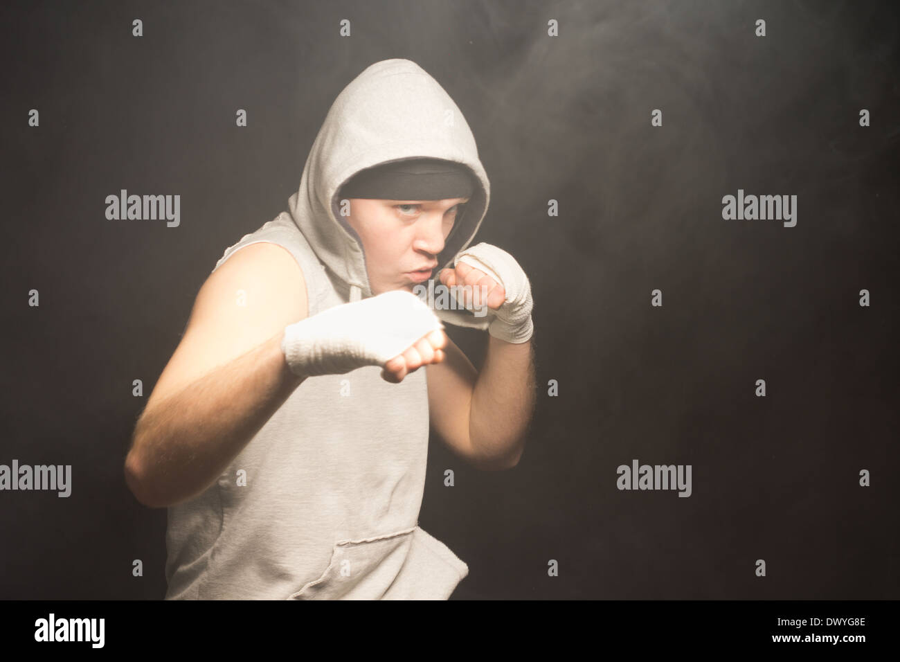 Pugnacious young boxer wearing a hooded top raising his bandaged fists ...
