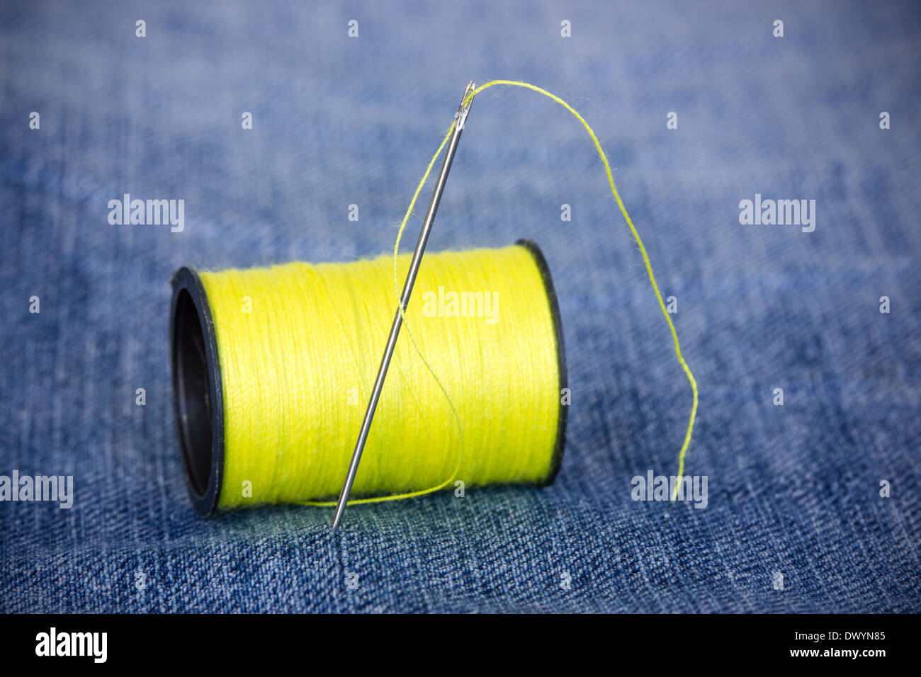 Needle with yellow thread on jeans material Stock Photo - Alamy